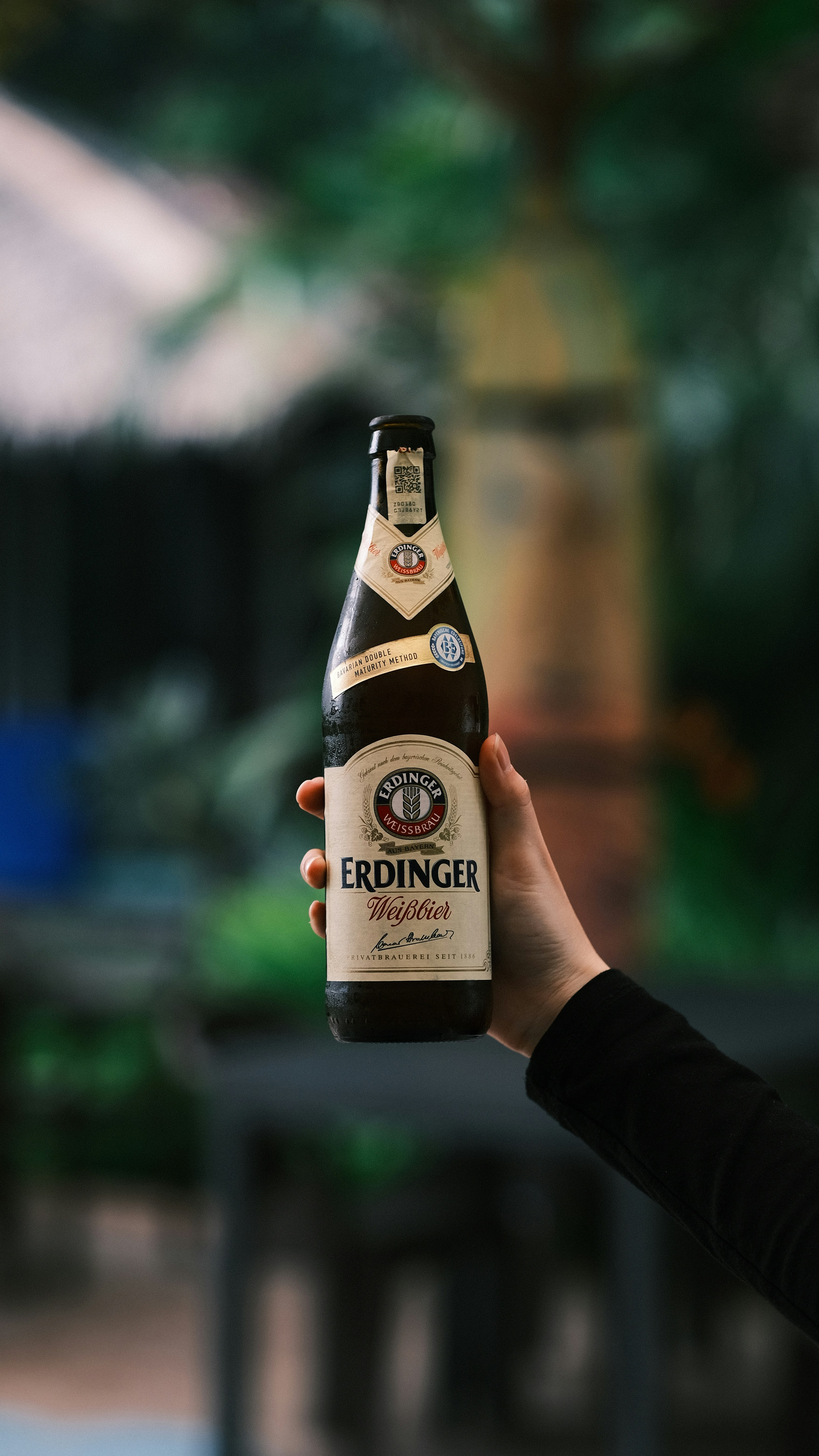 Erdinger in Hand: A Quiet Toast Against Velvet Garden Bokeh