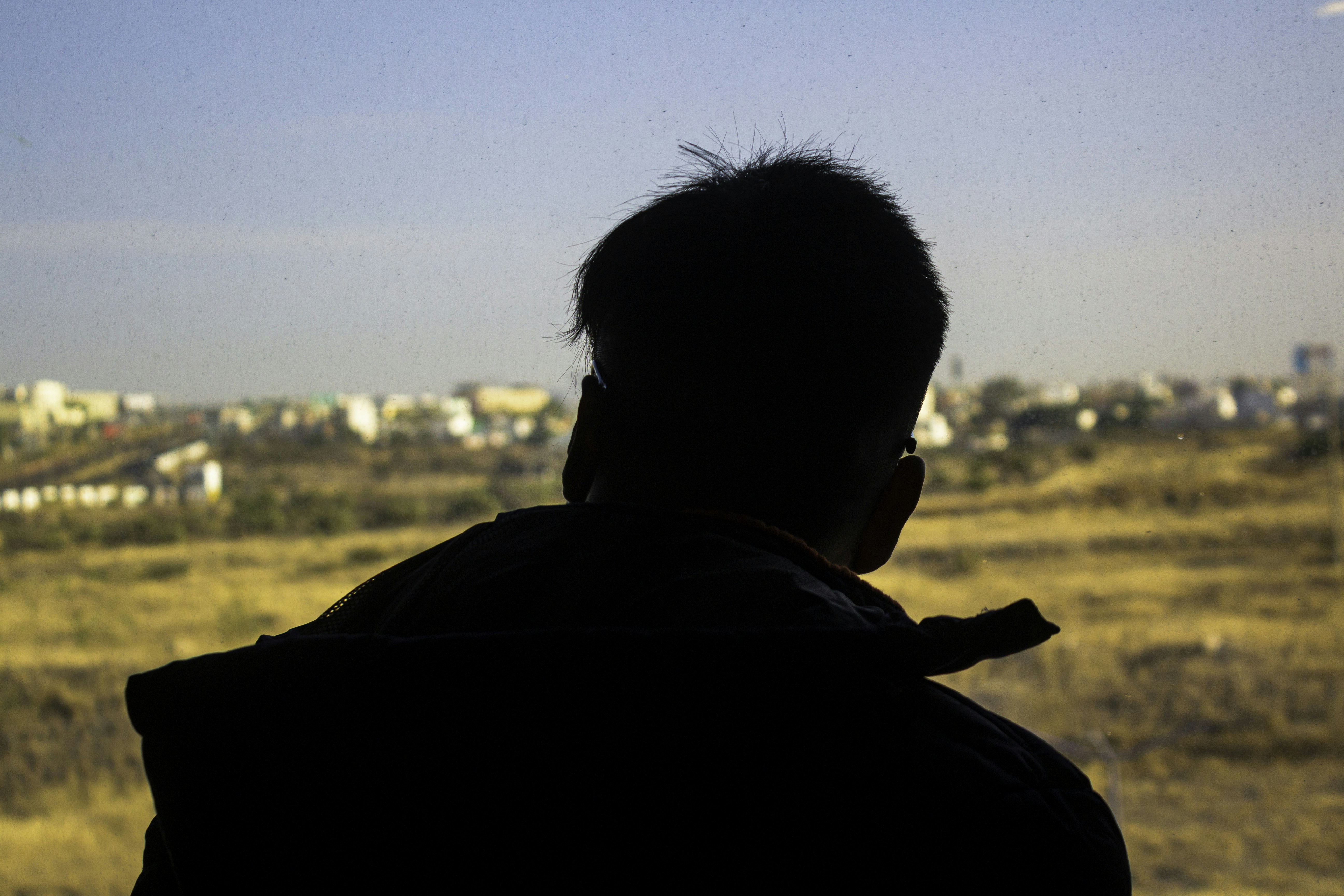 Silhouette of a person gazing over an expansive urban landscape under a clear blue sky.