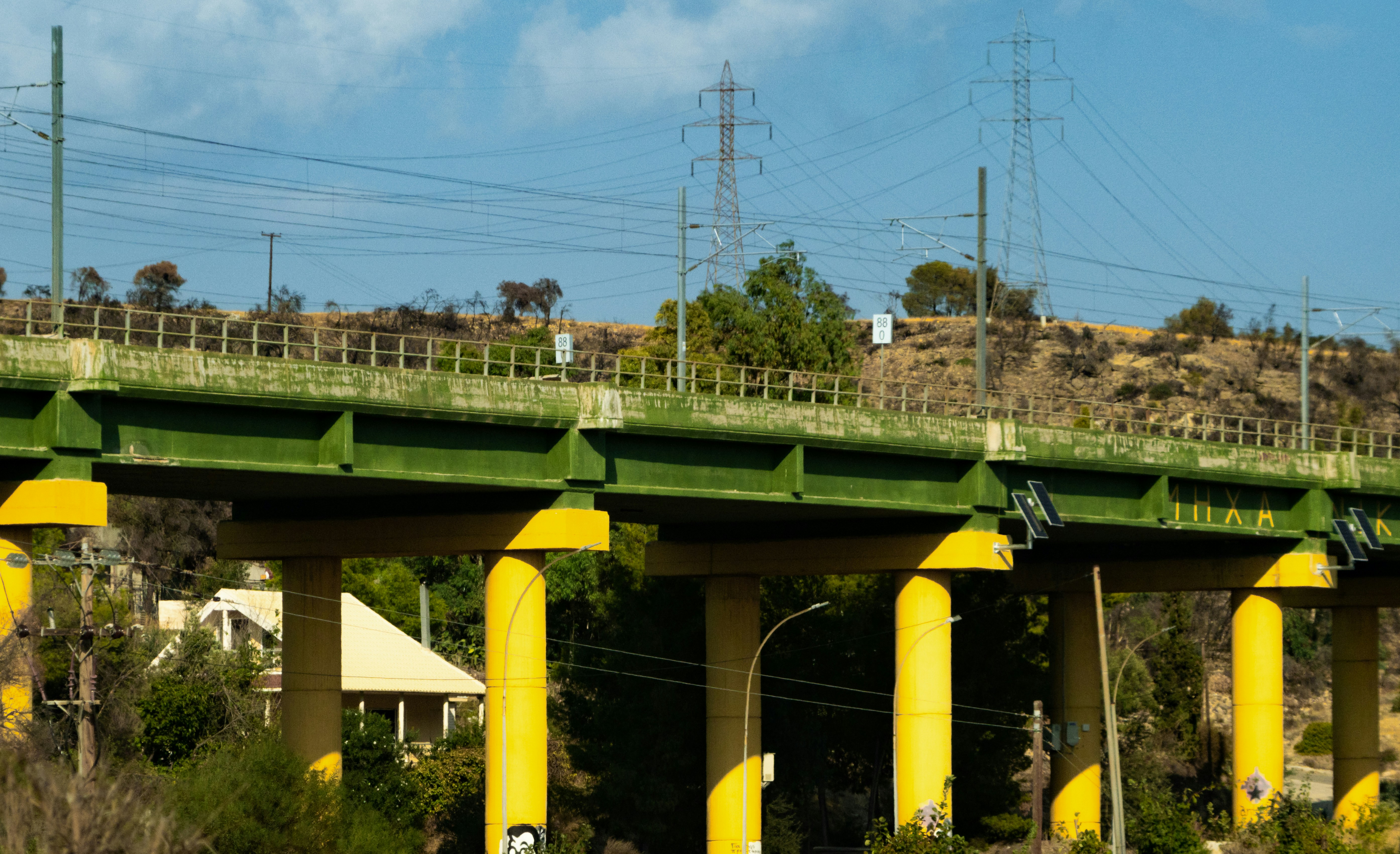 Sunlit Green Span: Yellow-Pillar Overpass Framing a Quiet Valley