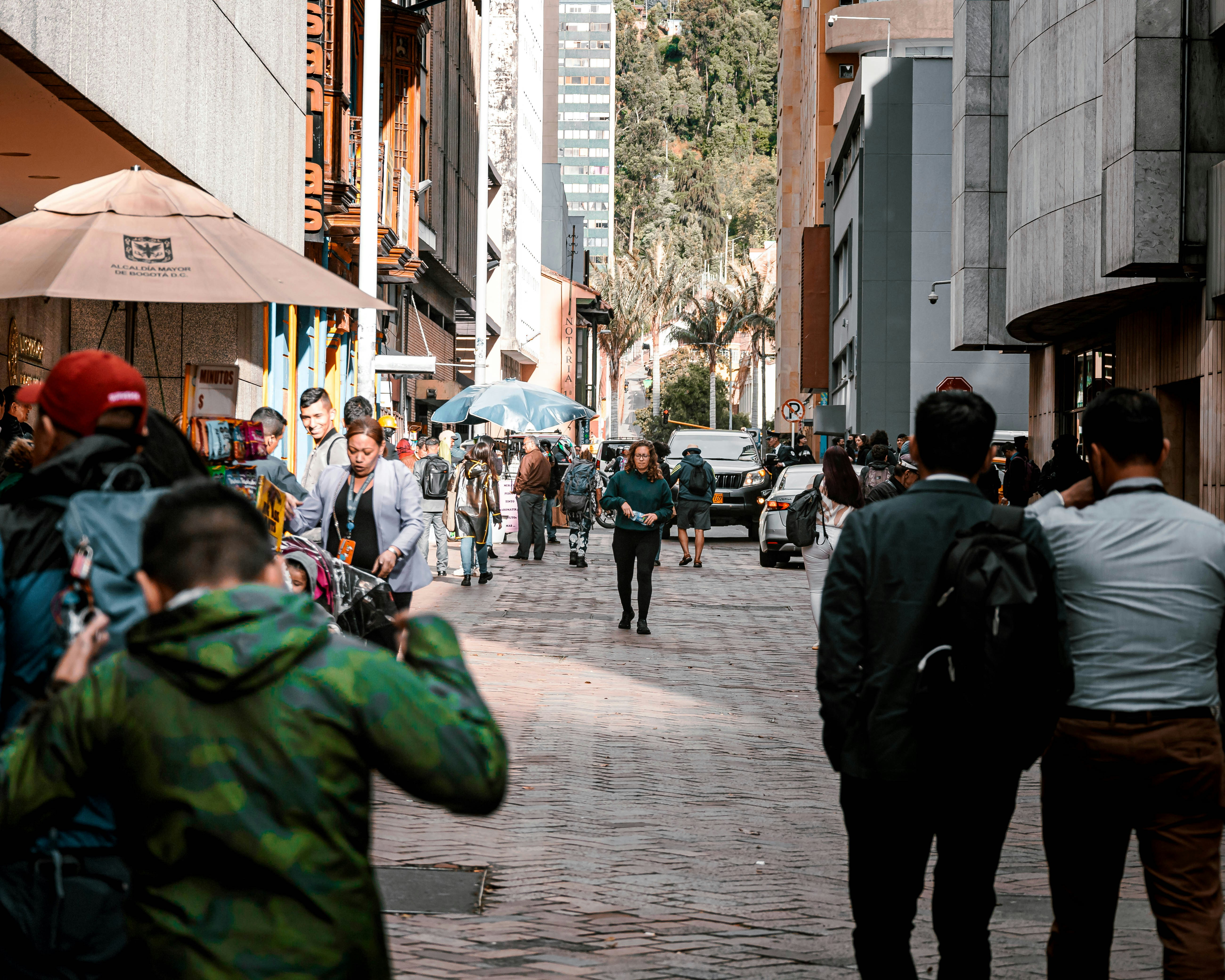 Pedestrians navigate a cobblestone street flanked by shops and vendors, against a backdrop of modern architecture.