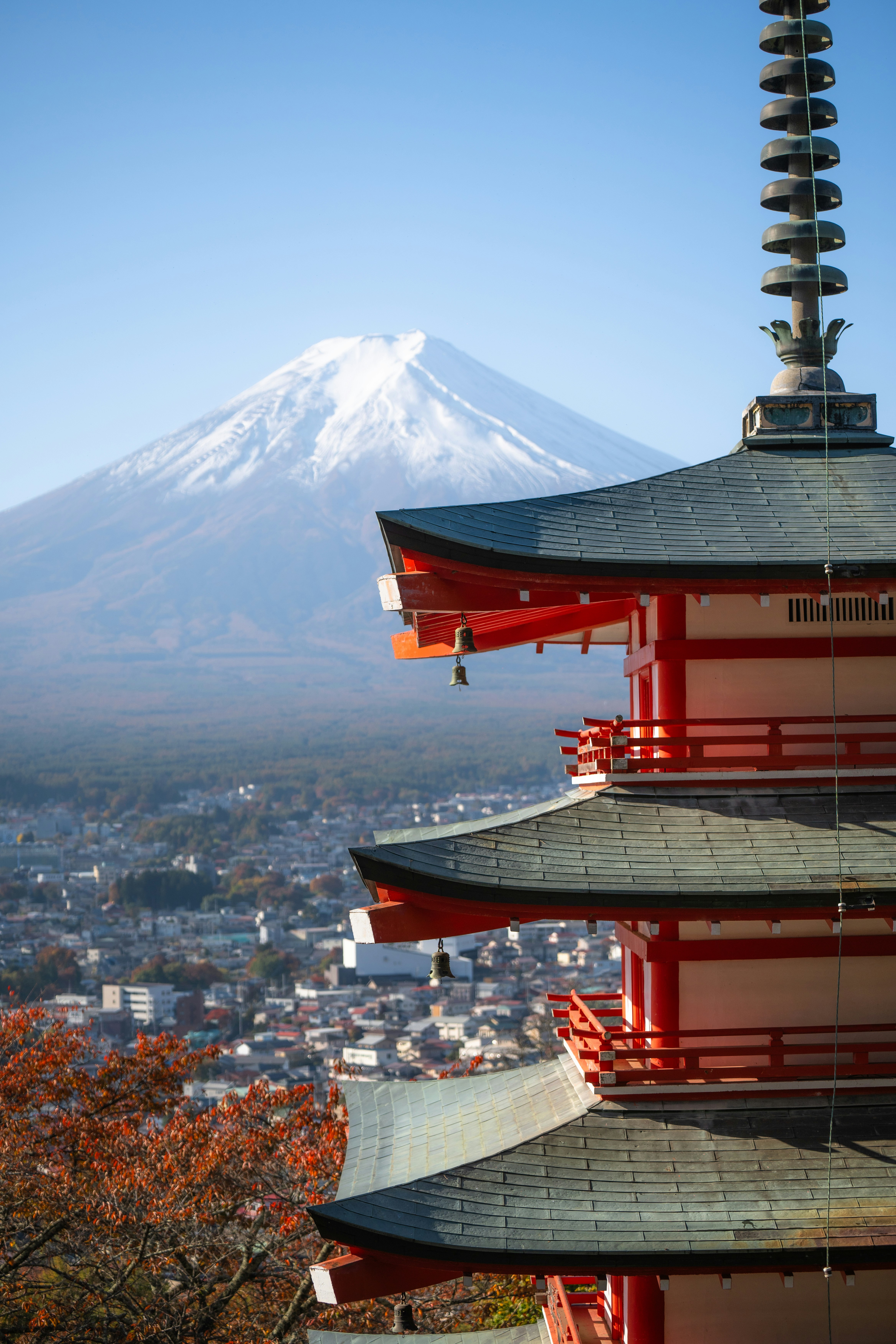 Red pagoda stands prominently against the backdrop of snow-capped Mount Fuji, framed by autumn foliage. The scene captures the serene coexistence of cultural heritage and natural beauty.