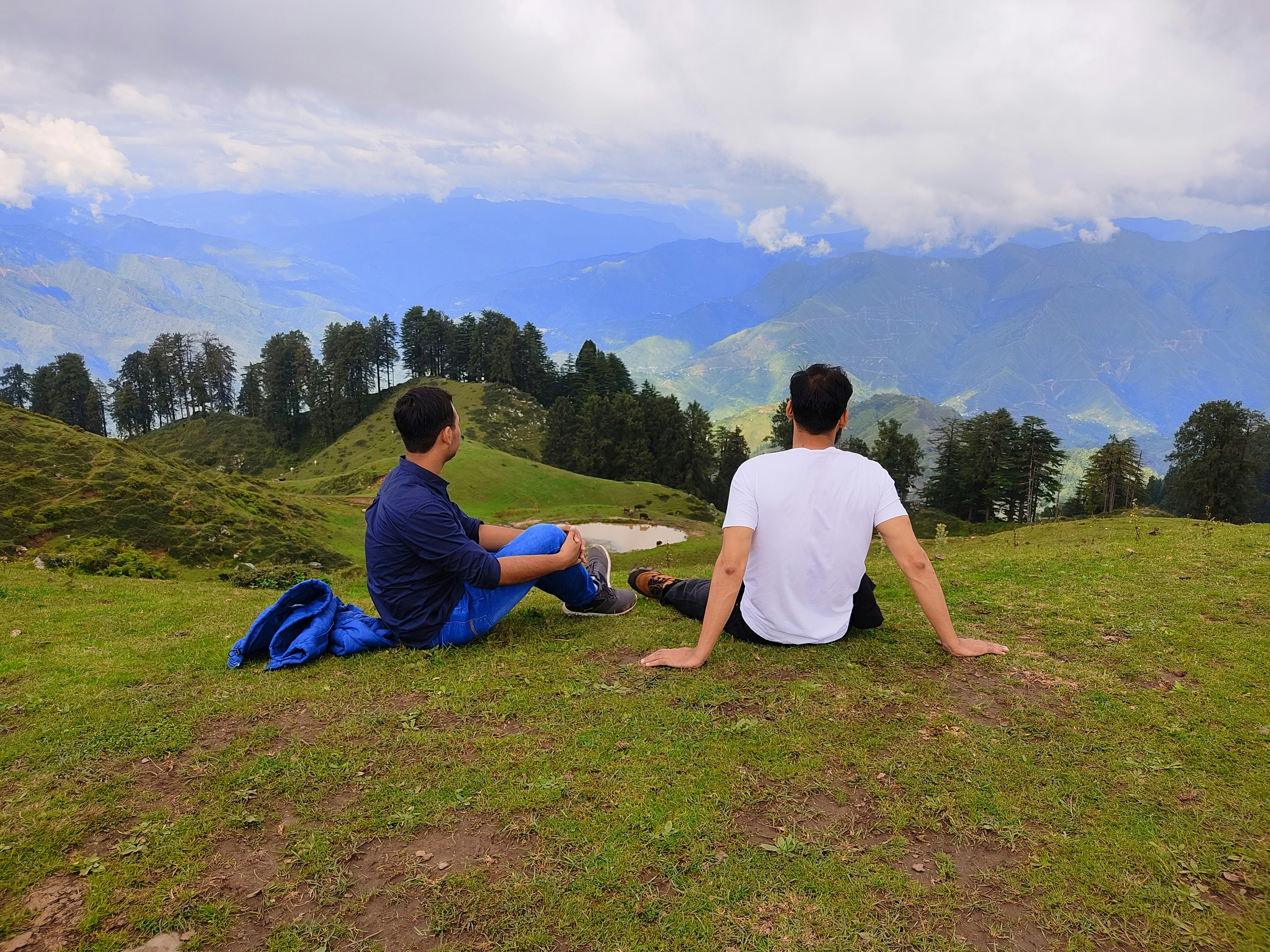 Two persons sitting on grassland and take rest after a long trekking they see beautiful scenery of mountains with Lush green forest
