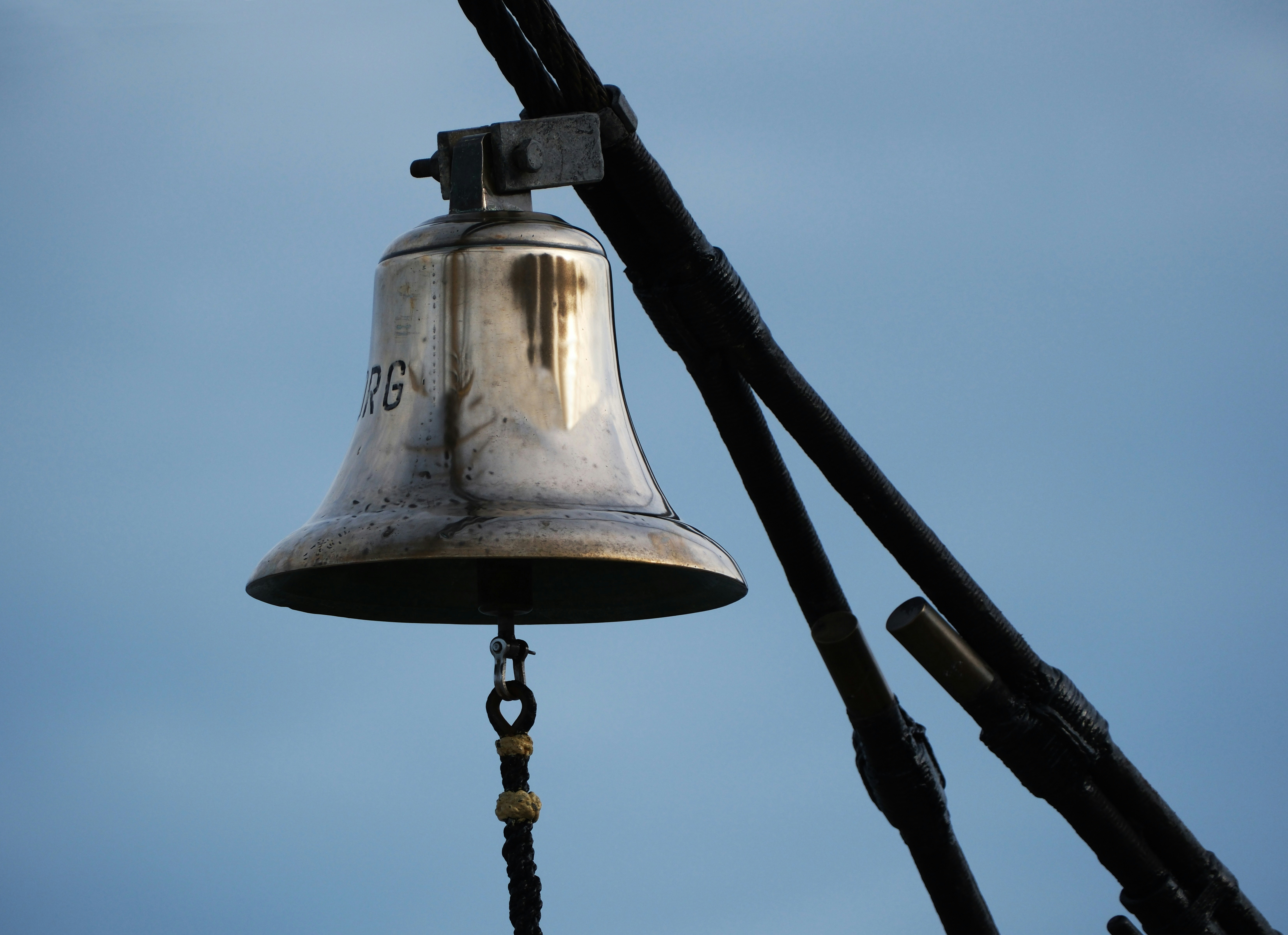 Weathered Bell Framed by Iron Lines Under a Calm Blue Sky