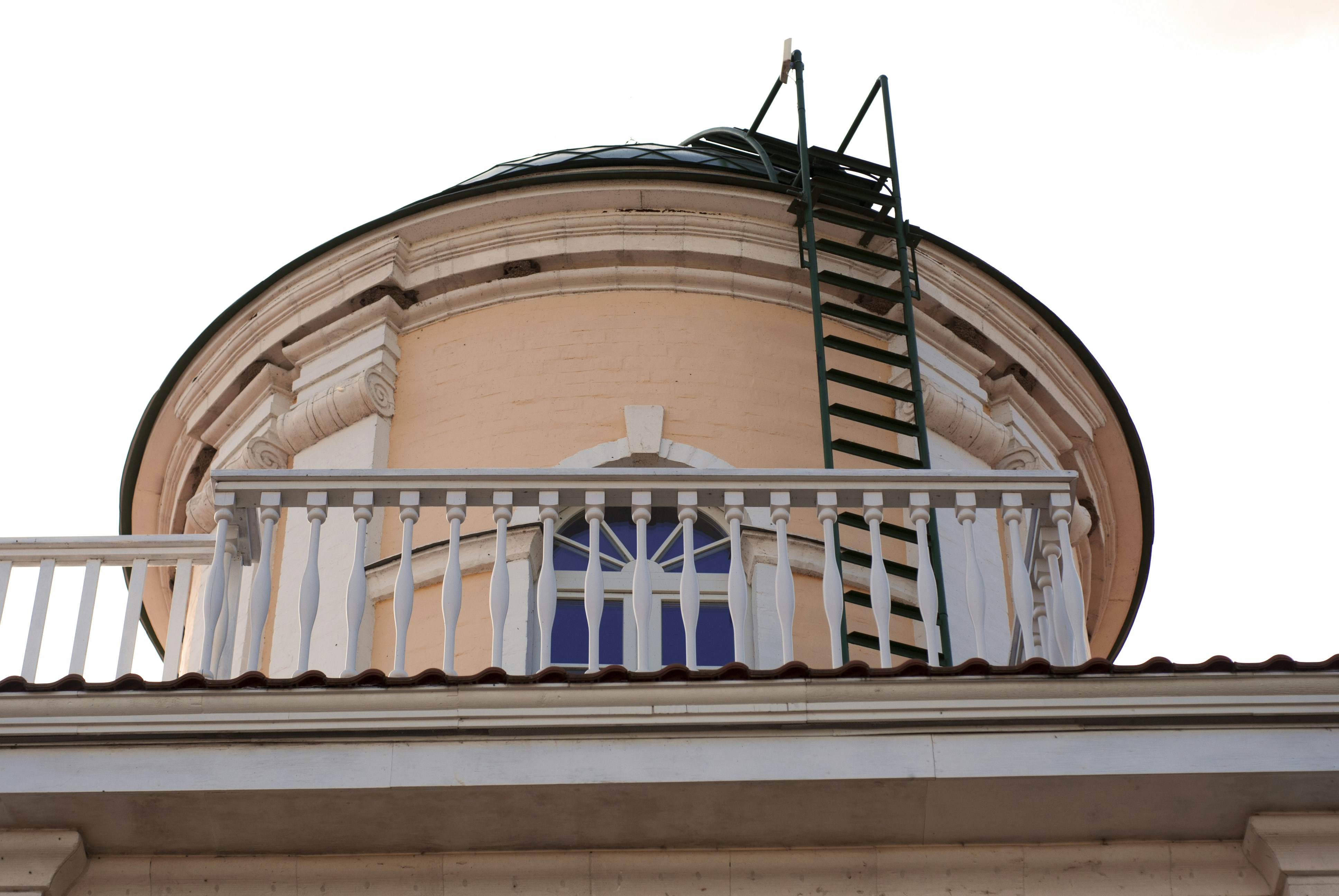 Round building with white balcony, blue door, and rooftop ladder against a clear sky.