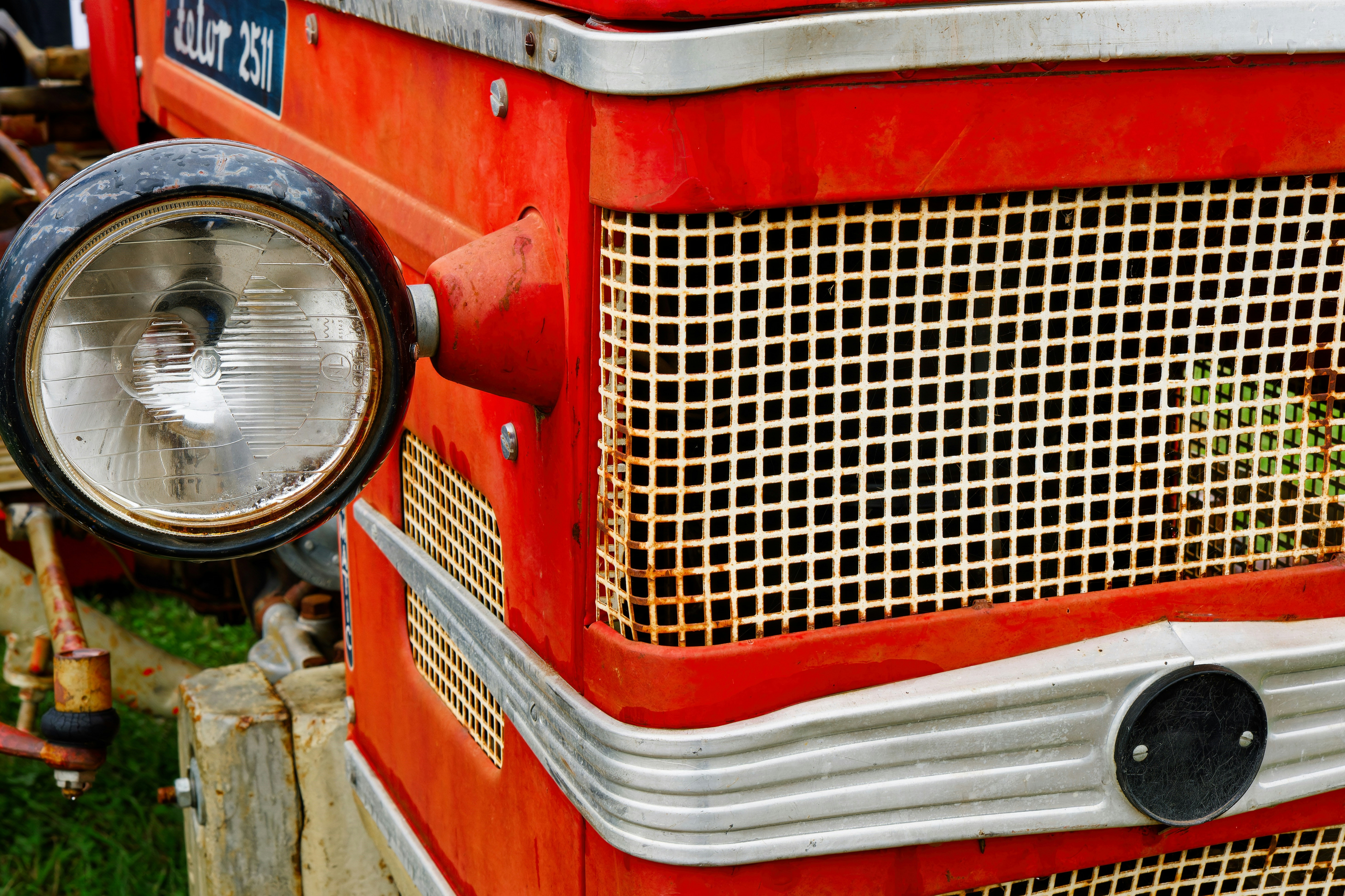 Close-up view of a vintage red tractor showcasing weathered details and unique features in a rural landscape during daylight - A vintage red tractor stands prominently in a grassy area, revealing its worn textures and charming characteristics under clear skies, reflecting rural life.