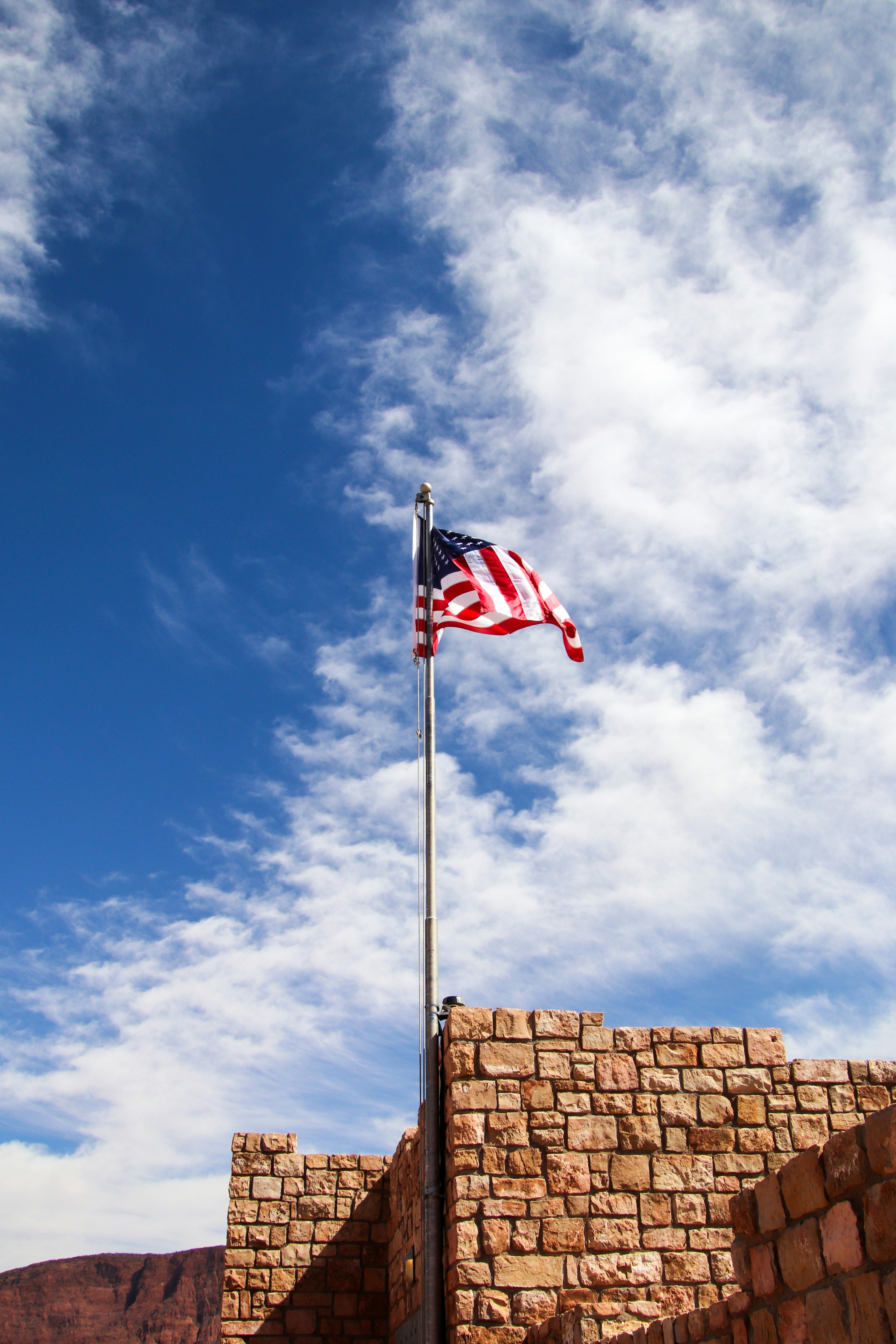 Flag atop a sunlit stone bastion beneath a vast blue sky