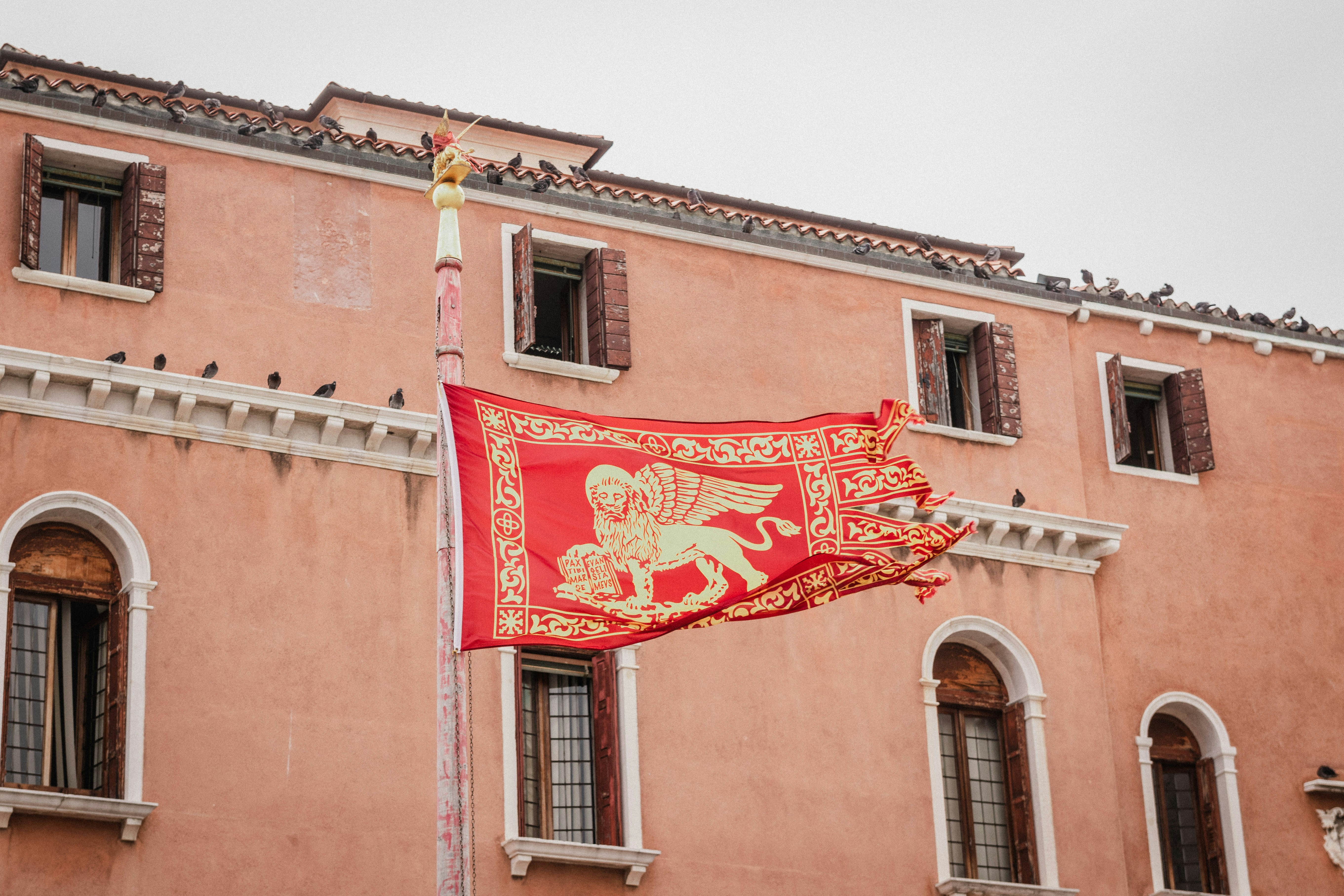 A red and gold flag on a pole in front of a building photo – Free ...