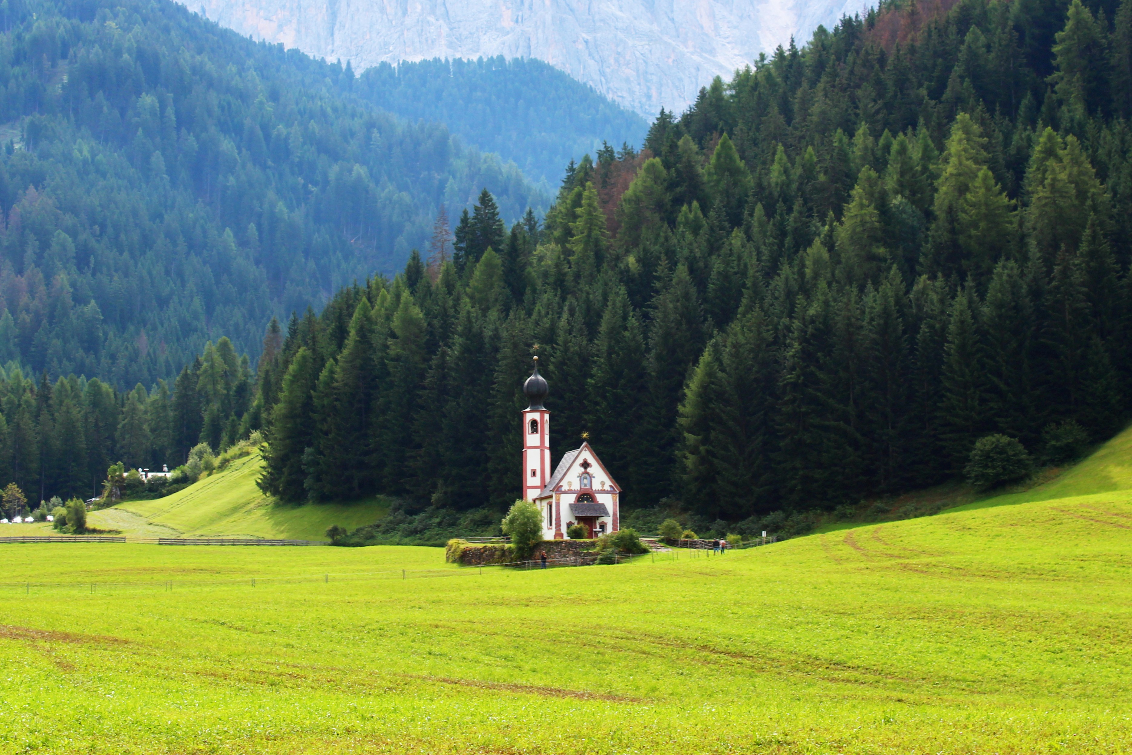 A church in the middle of a field with mountains in the background ...