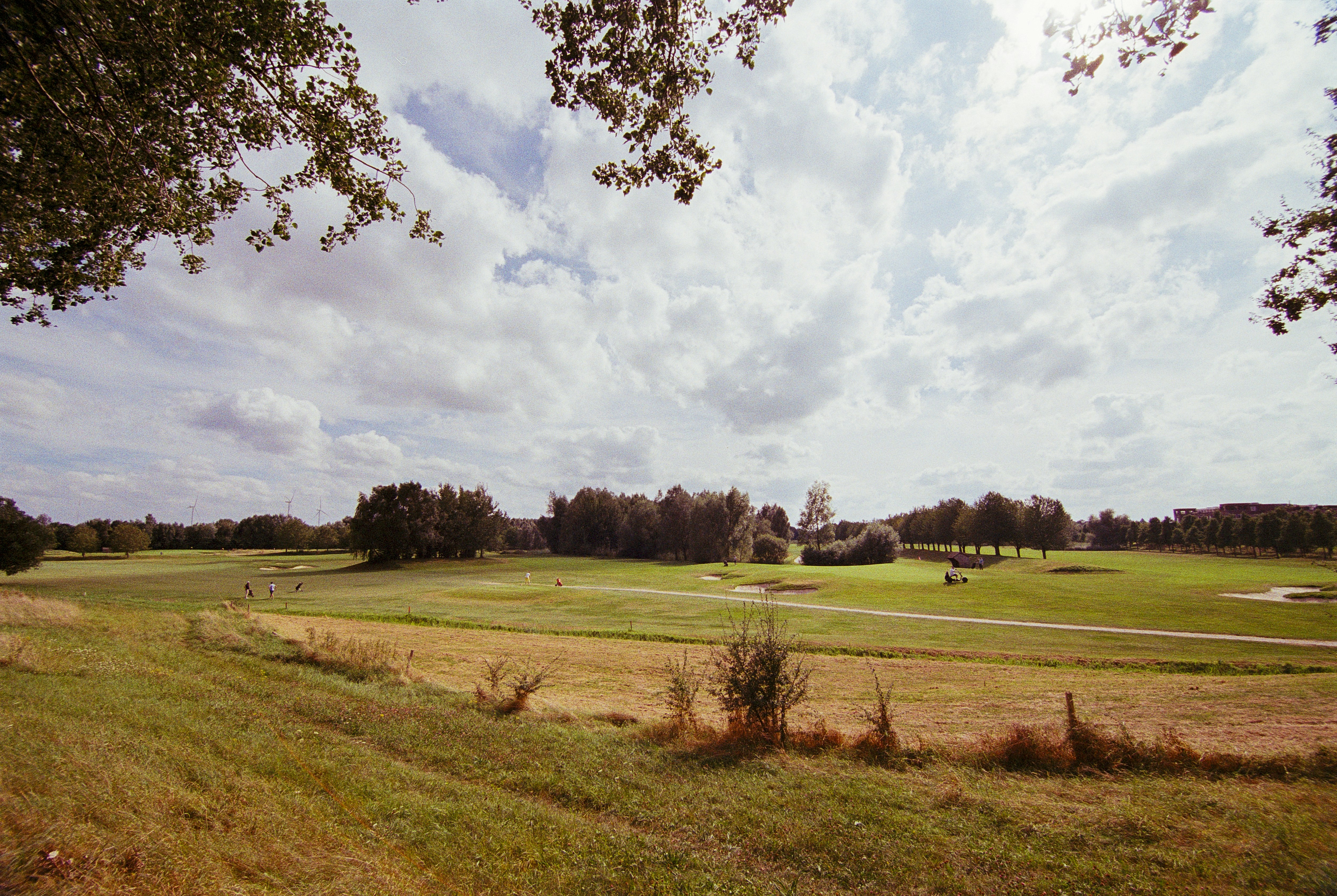 Expansive golf course under a sky filled with dramatic clouds and sunlit patches of grass.