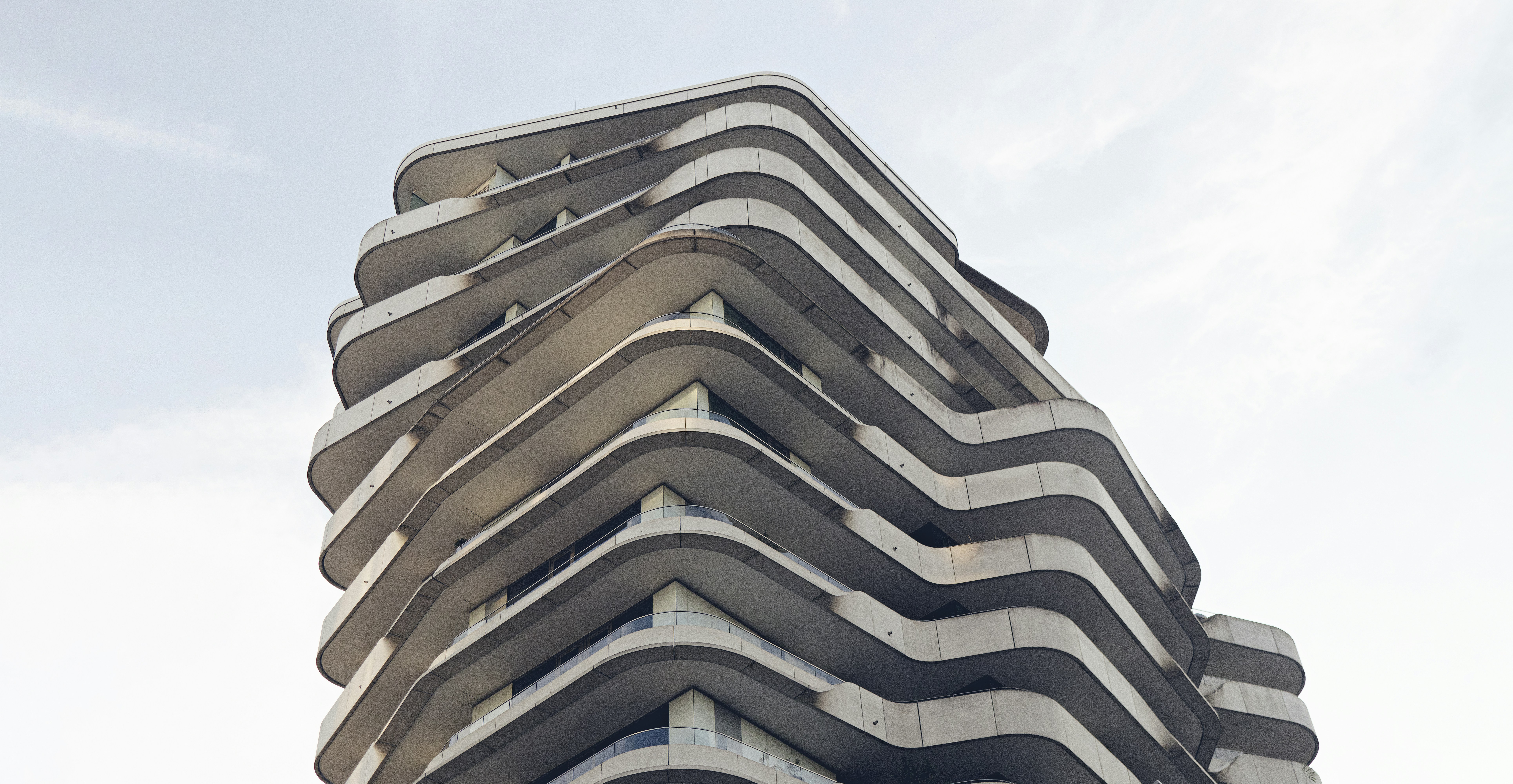 Architectural shot of a high-rise with staggered, curved balconies forming a repeating wave pattern against a pale sky.