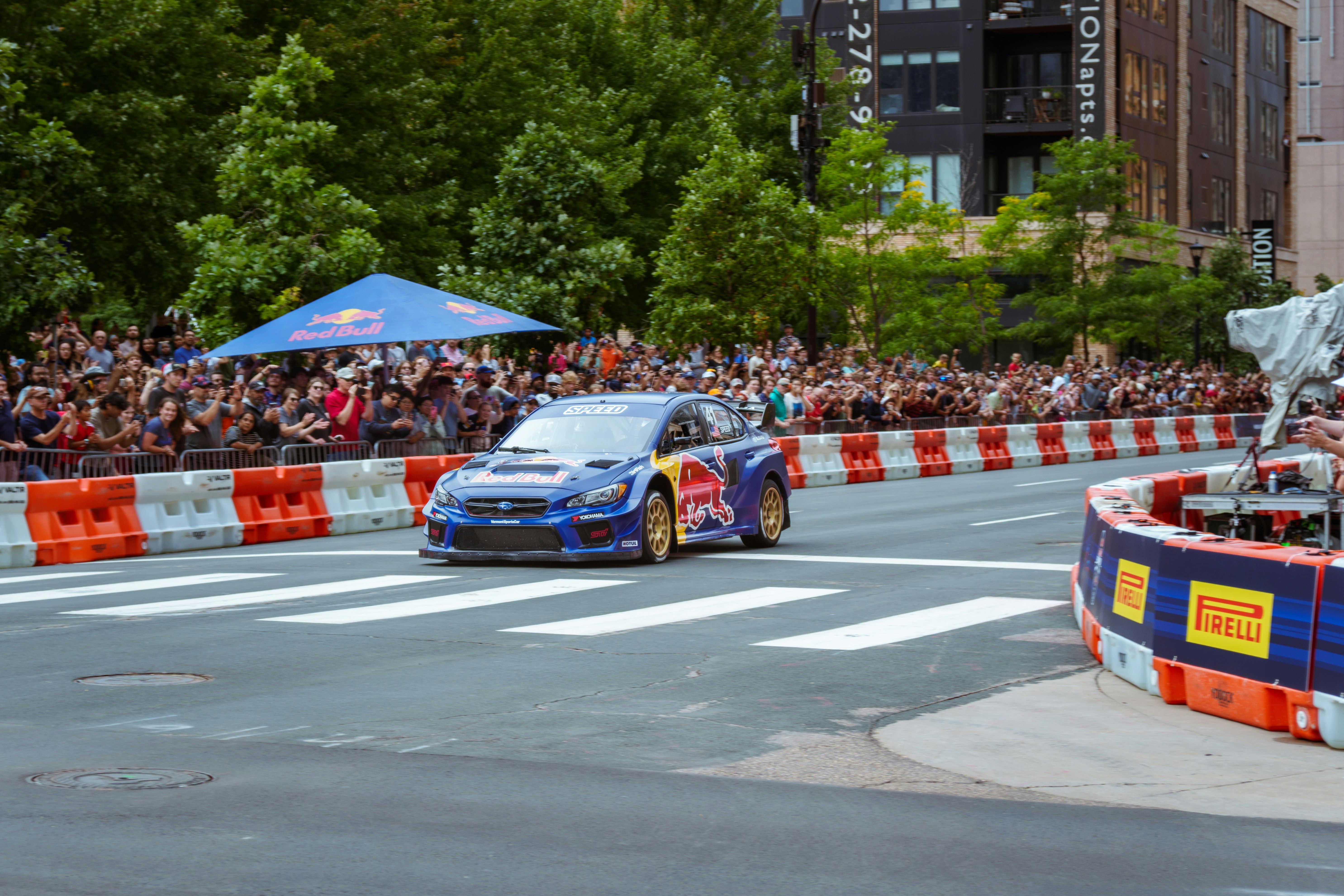A couple of cars driving down a street next to a crowd of people photo ...