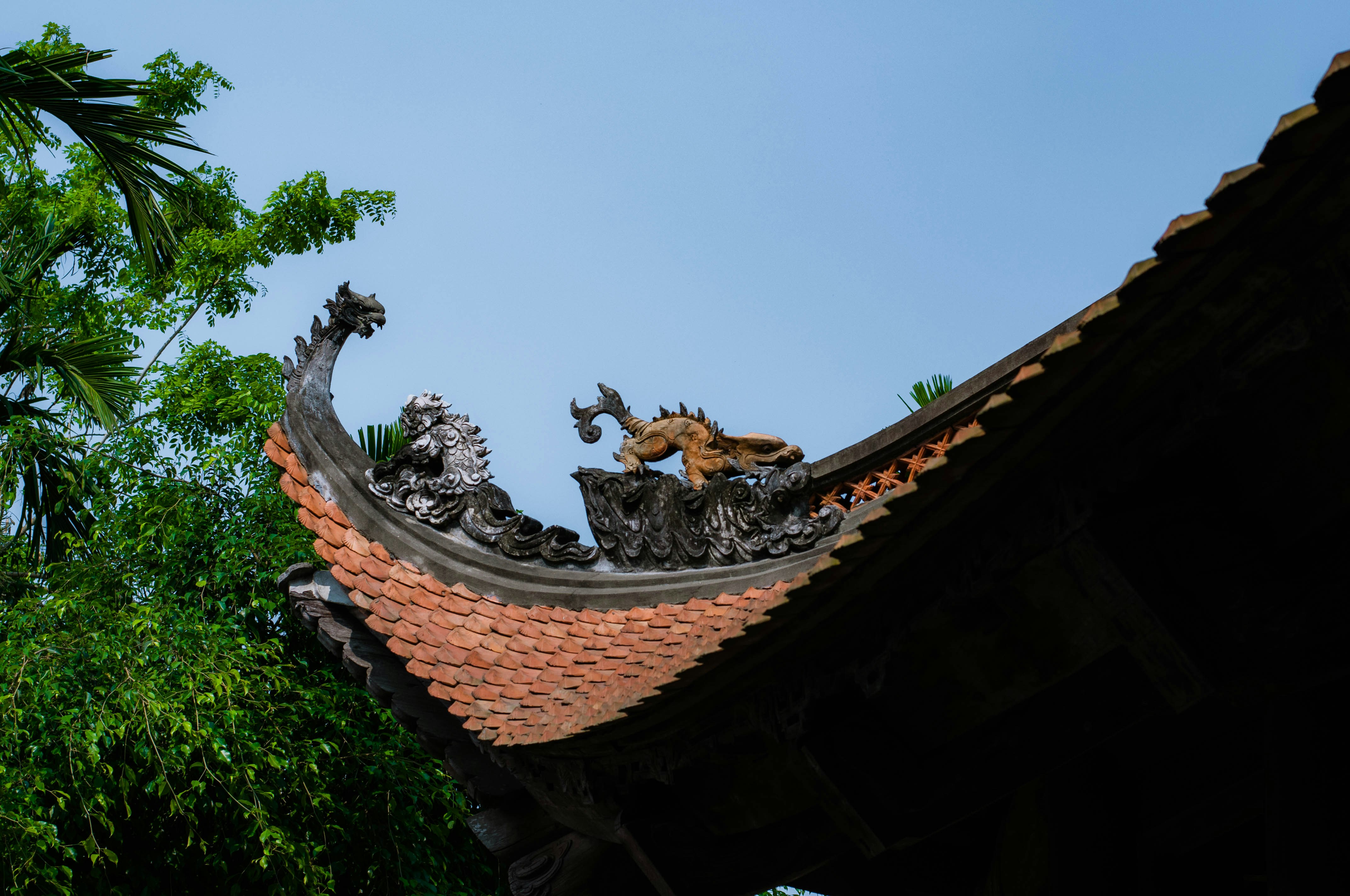 Intricately carved figures atop the Mông Phụ Communal House roof under a clear blue sky.