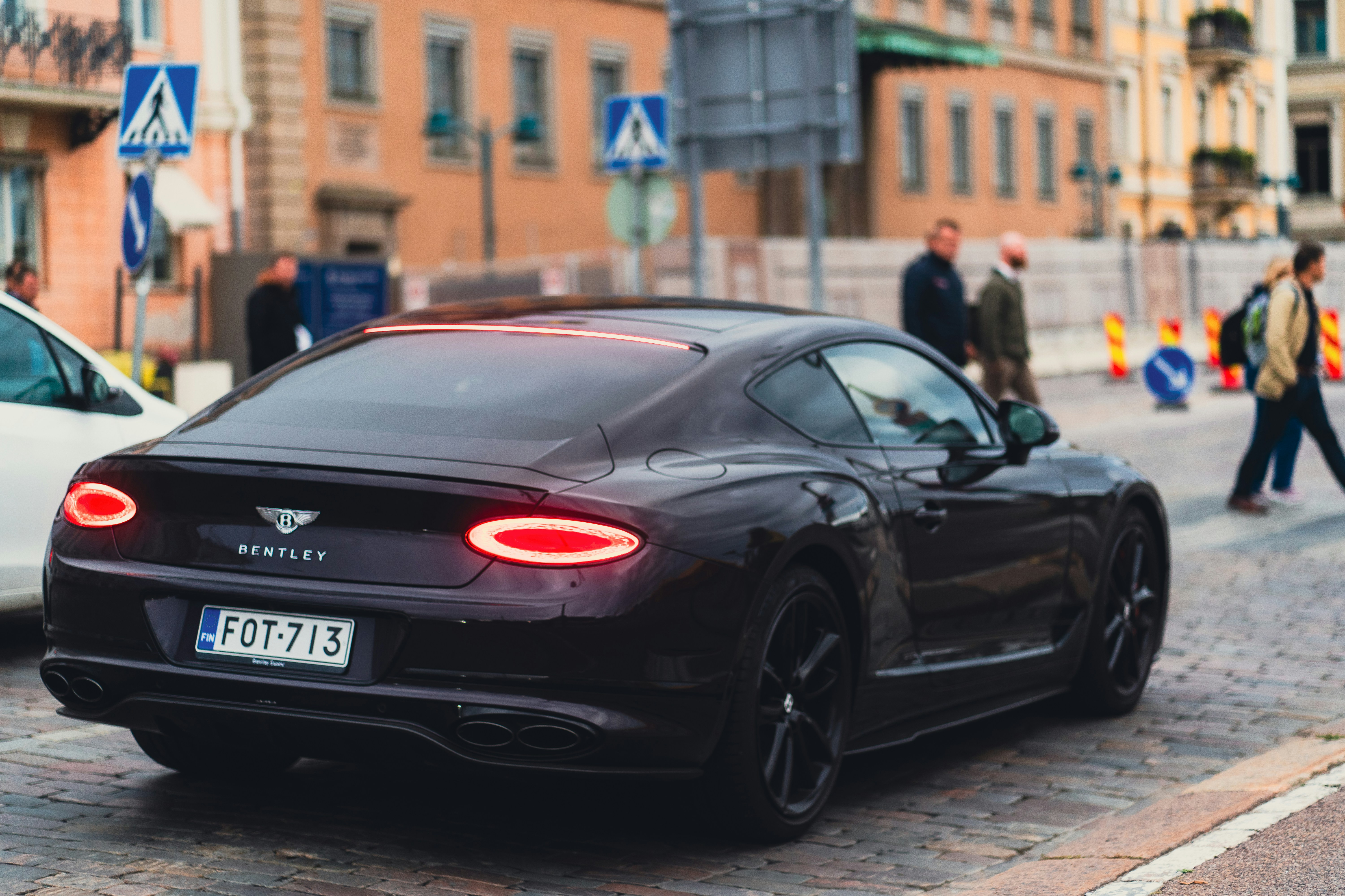 Sleek black Bentley parked on a cobblestone street, showcasing its luxury design against an urban backdrop.
