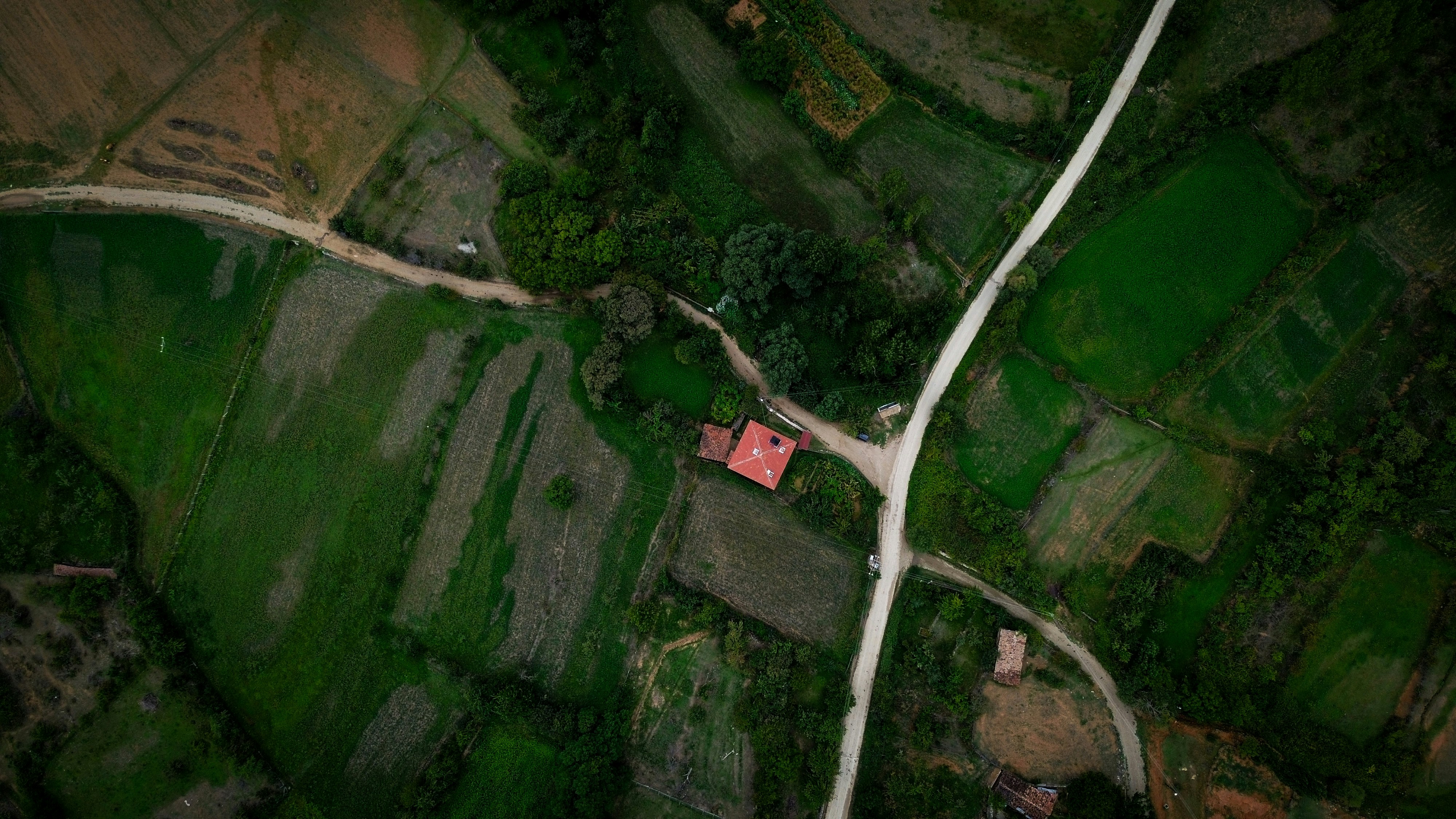 Aerial view of a rural landscape featuring a red-roofed house surrounded by lush green fields and intersecting roads.