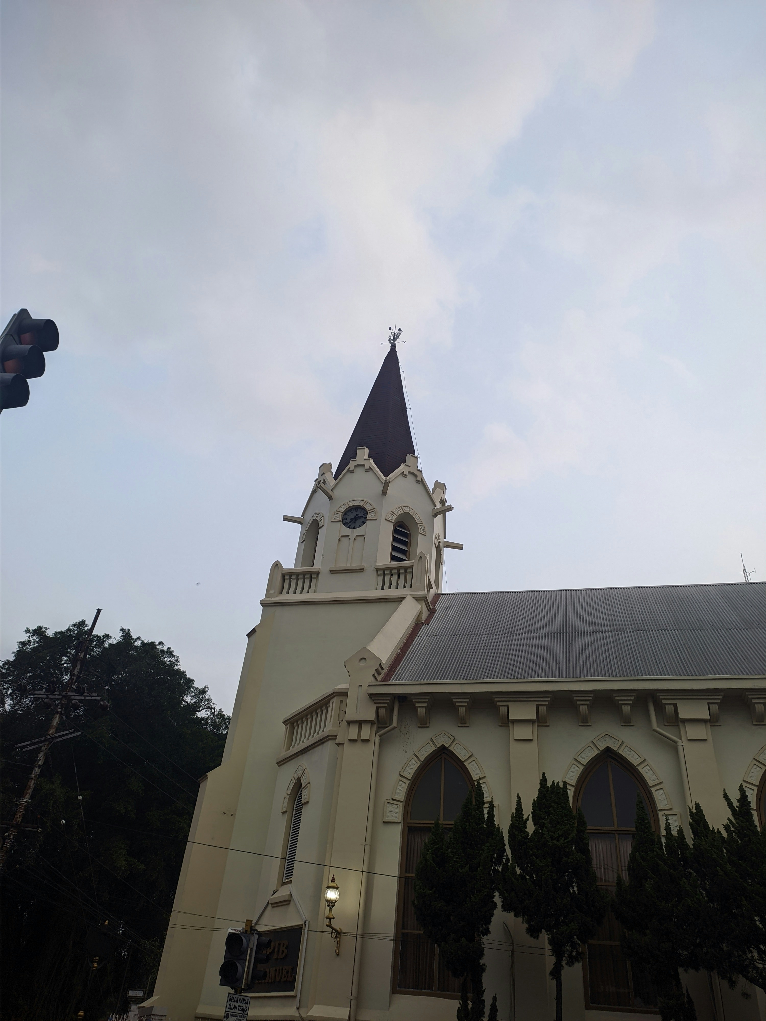Historic church with a prominent steeple against a cloudy sky, framed by lush greenery and urban elements.
