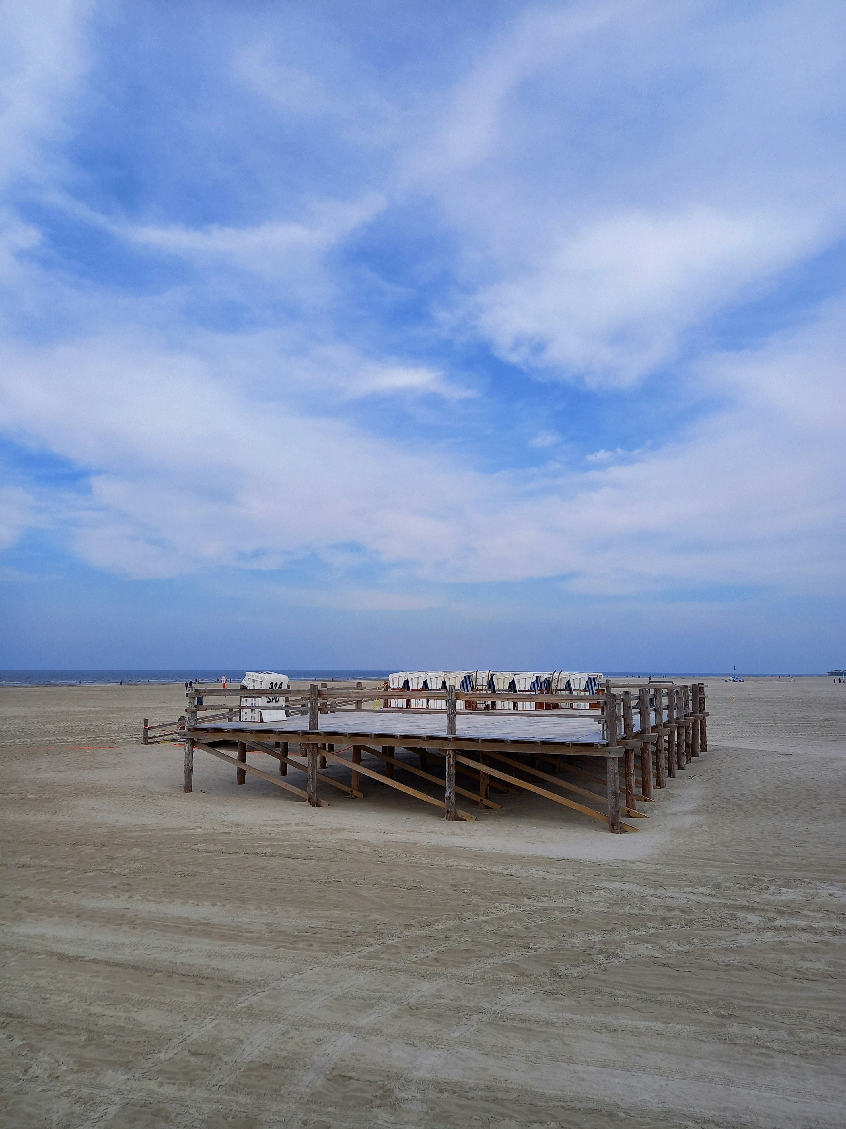 Wooden pier and beach tents under a sweeping coastal sky