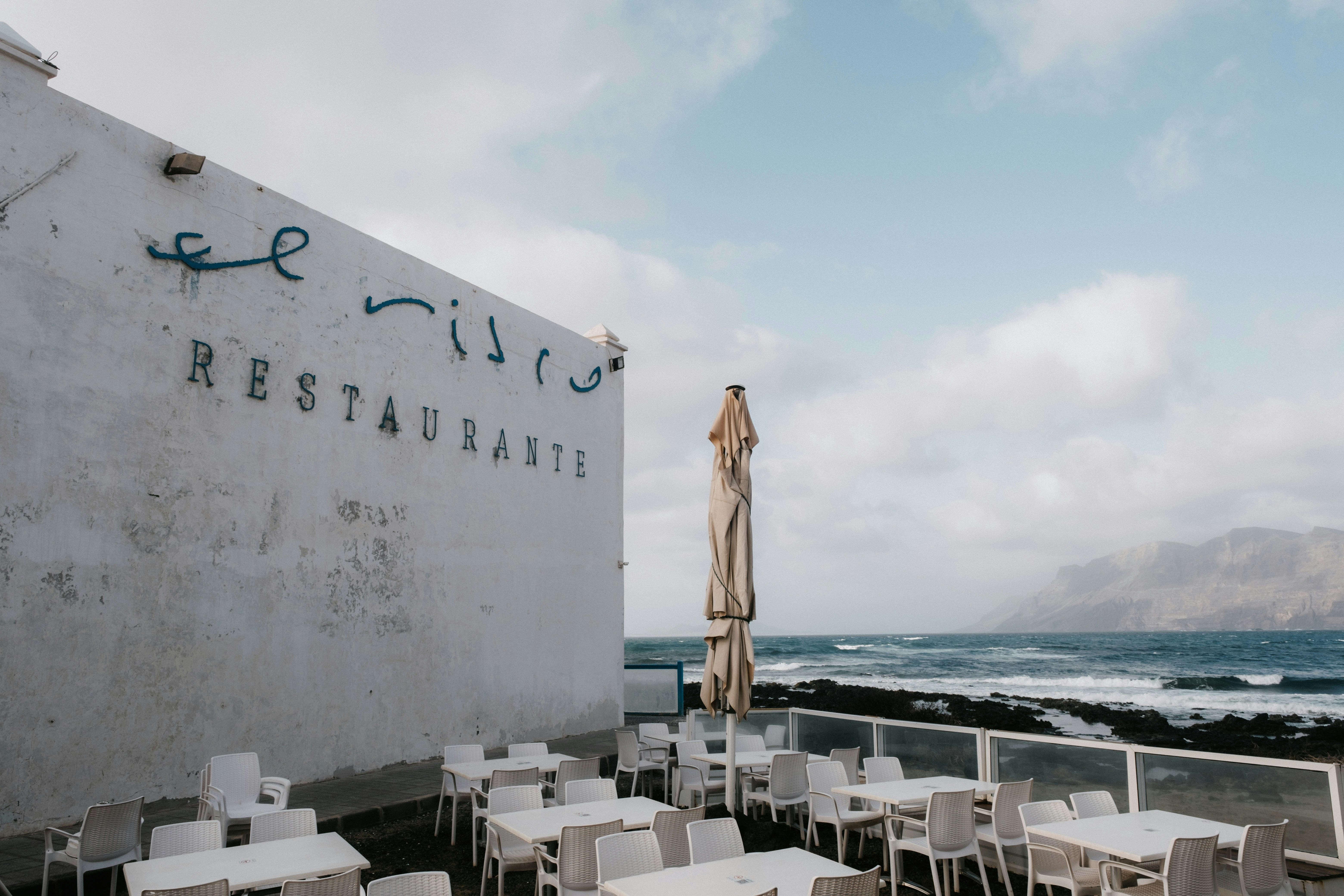 Seaside bistro at dusk: white chairs, weathered wall, and calm horizon