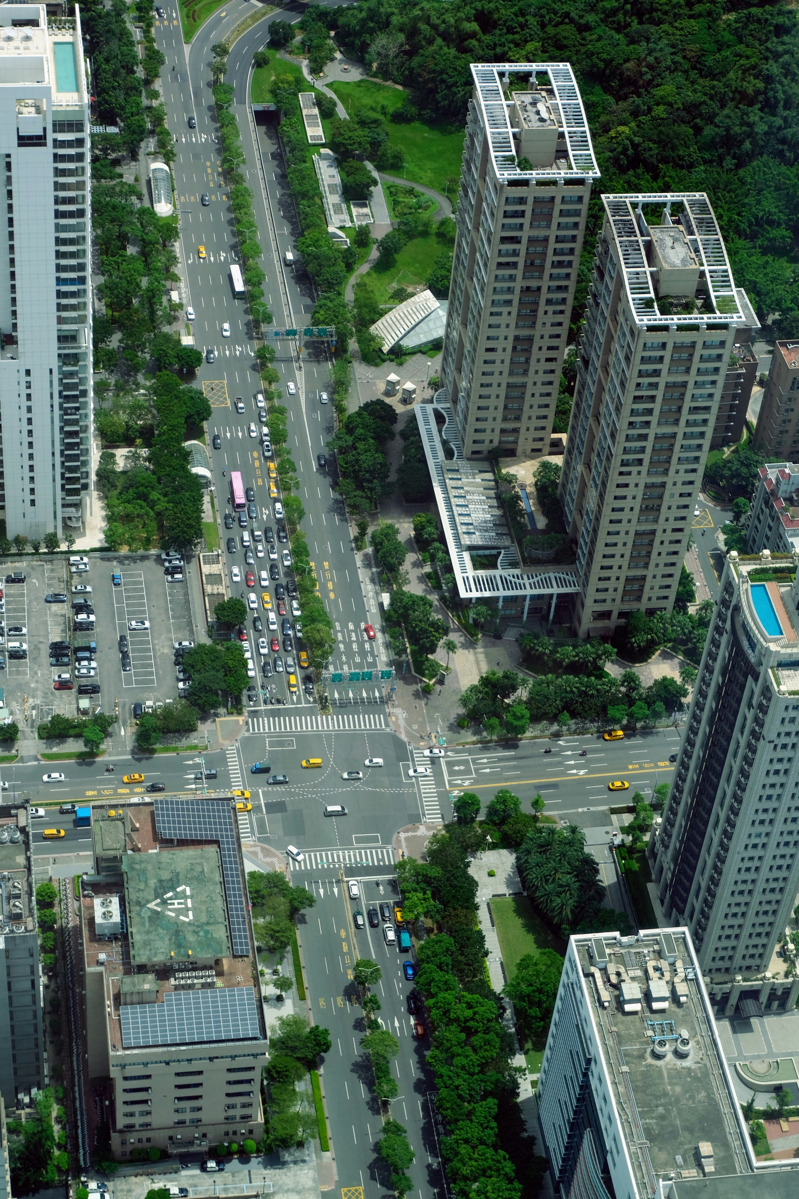 Aerial view of a bustling city intersection surrounded by modern skyscrapers and lush greenery, showcasing the vibrant flow of urban traffic.