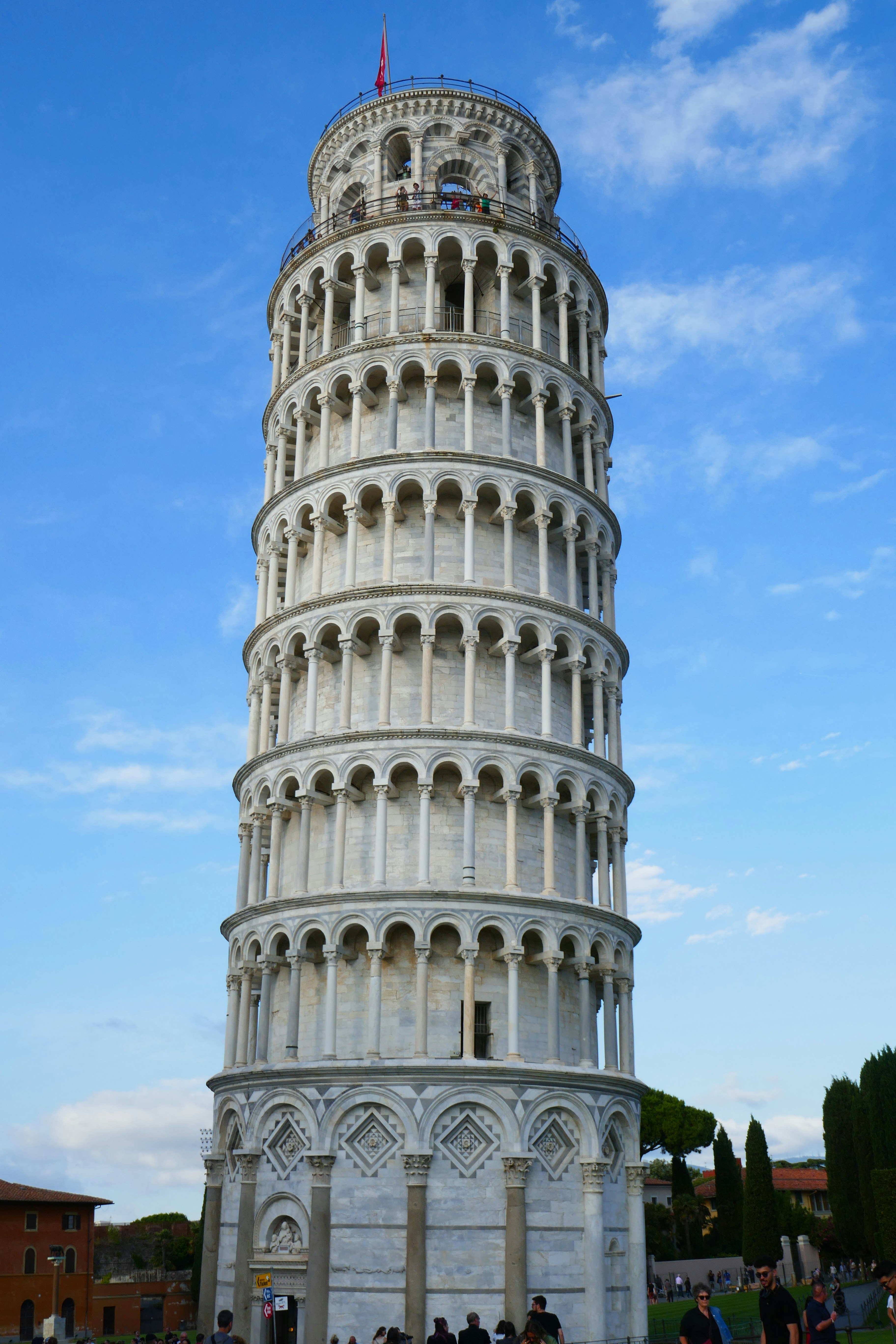 A photograph of the Leaning Tower of Pisa against a bright blue sky, its stacked arches creating rhythm along the marble exterior.