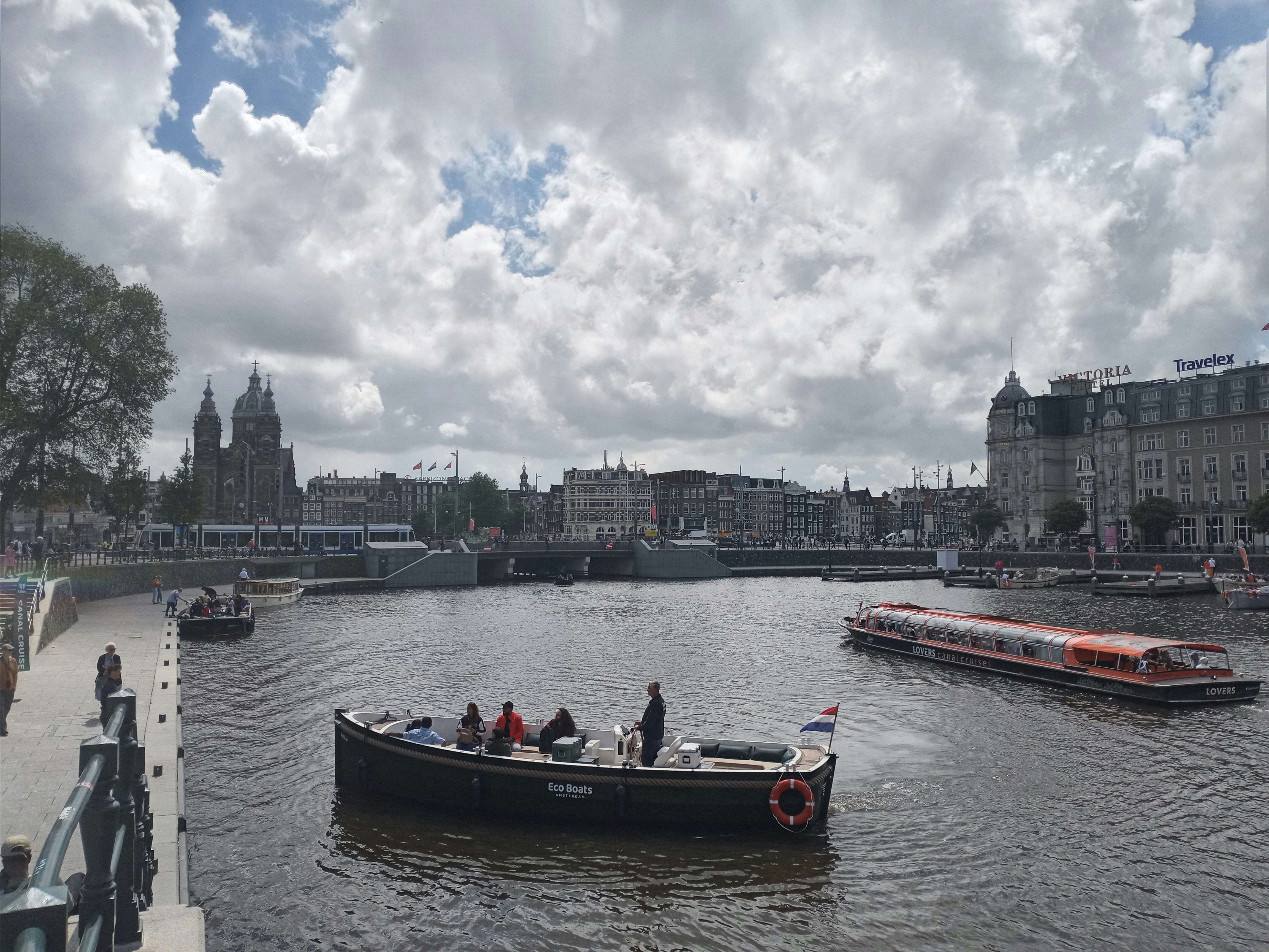 Canal Parade: Tour Boat Drifts by Amsterdam's Cloud-Washed Waterfront