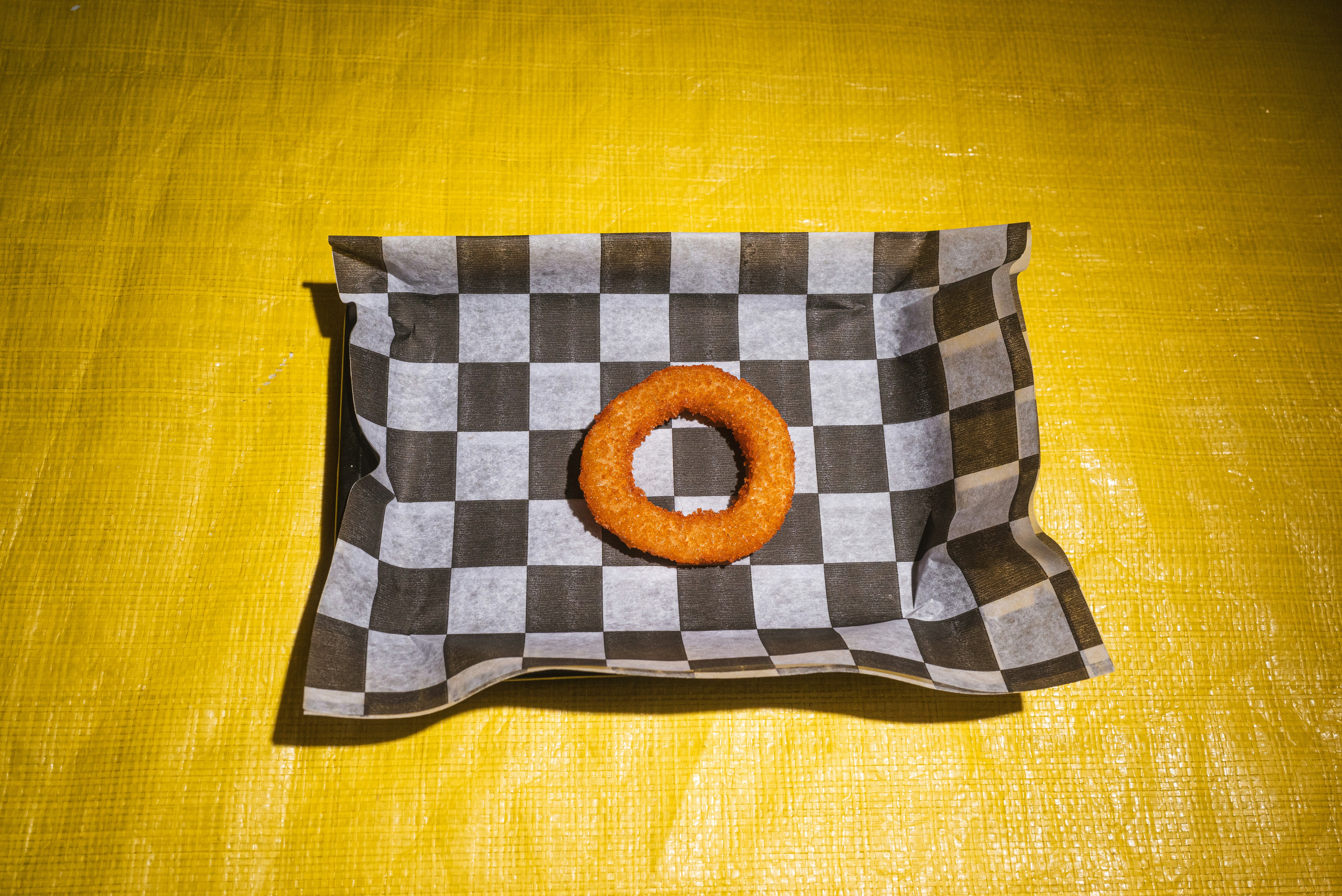 Center Ring on a Checkered Stage: A Crisp Onion Ring on a Sunny Yellow Backdrop