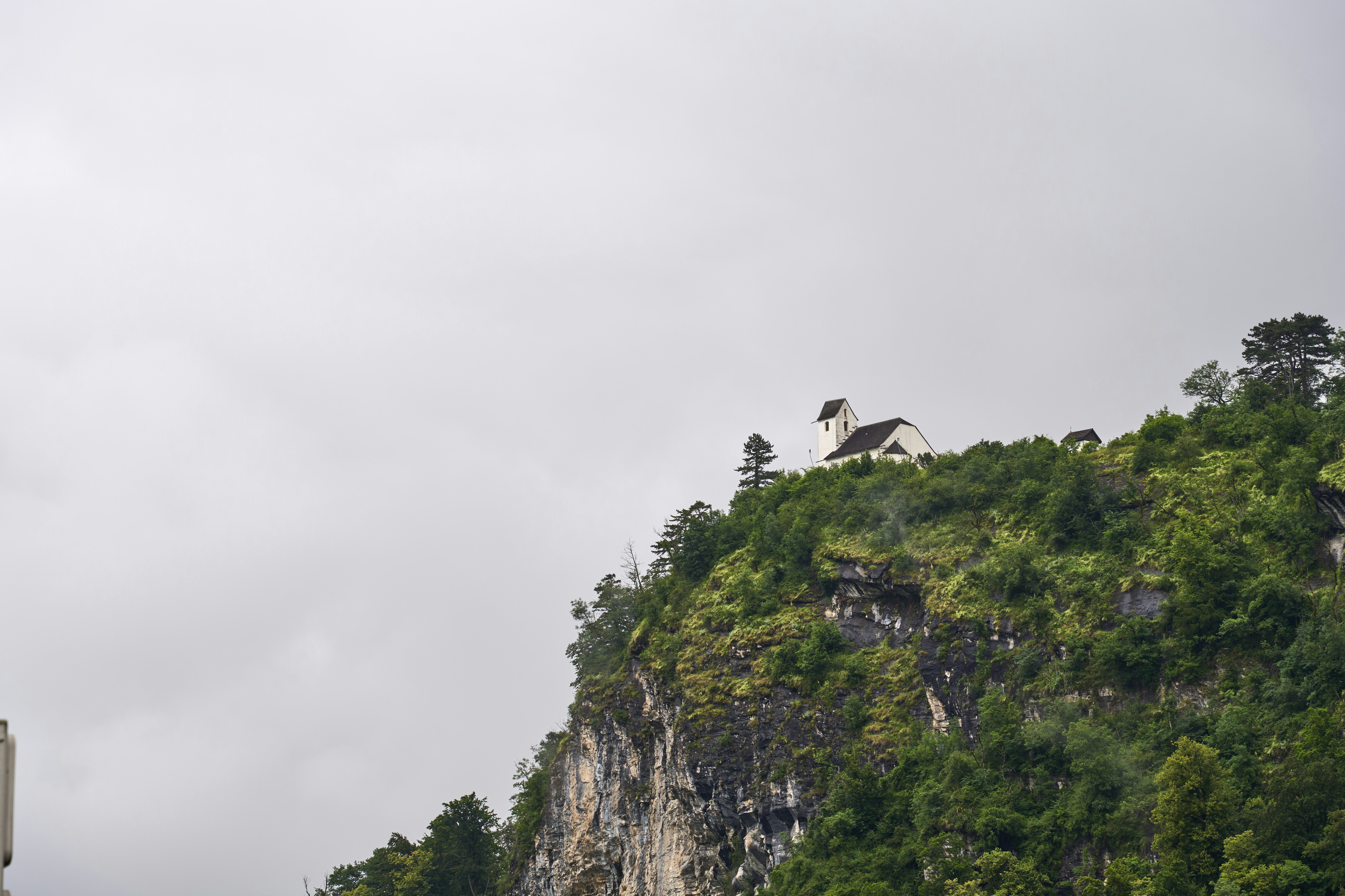 Cliffside Crest: A Quiet House Crowned by Green Slopes Under Gray Skies