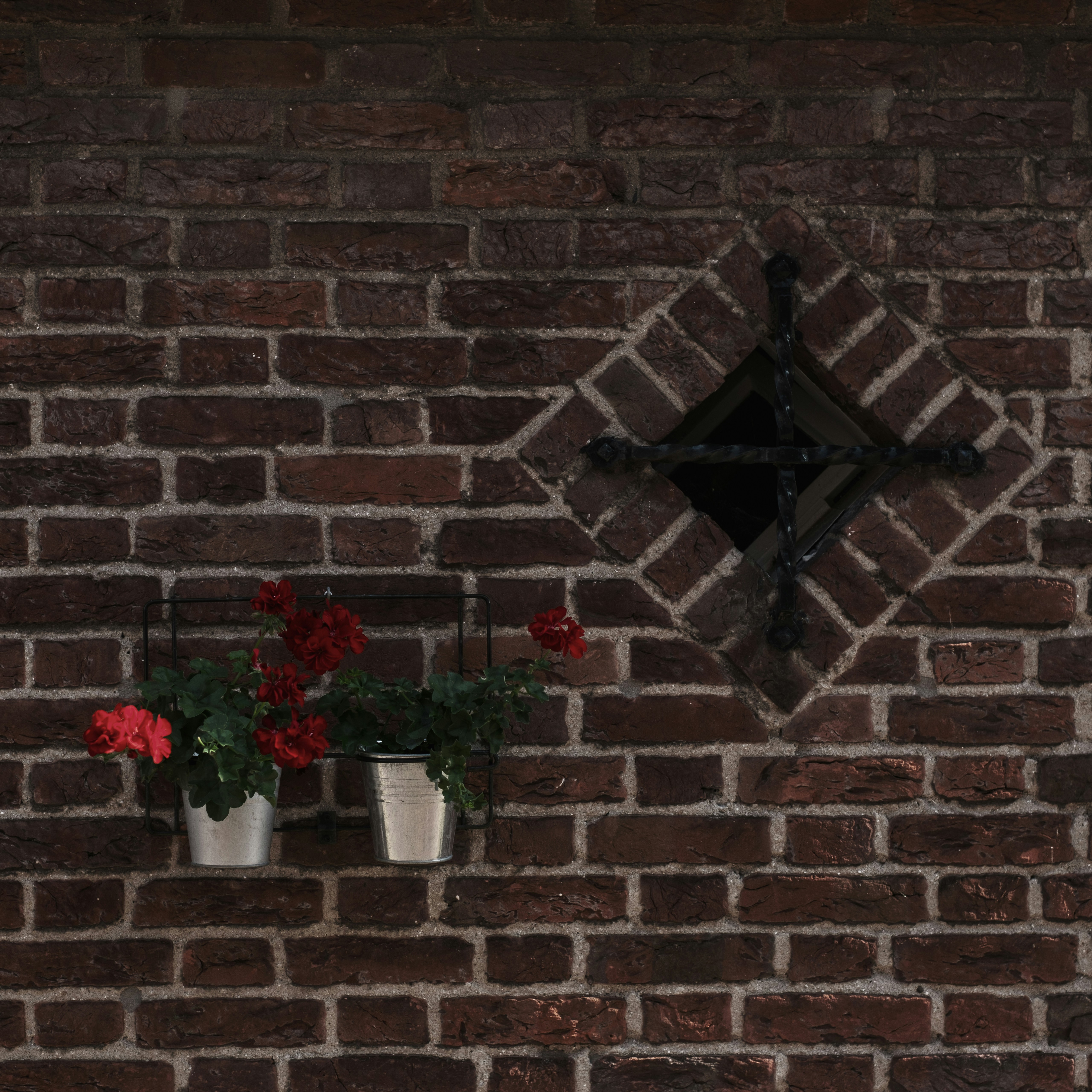 Wrought-Iron Diamond on Weathered Brick Wall, Framed by Red Geraniums