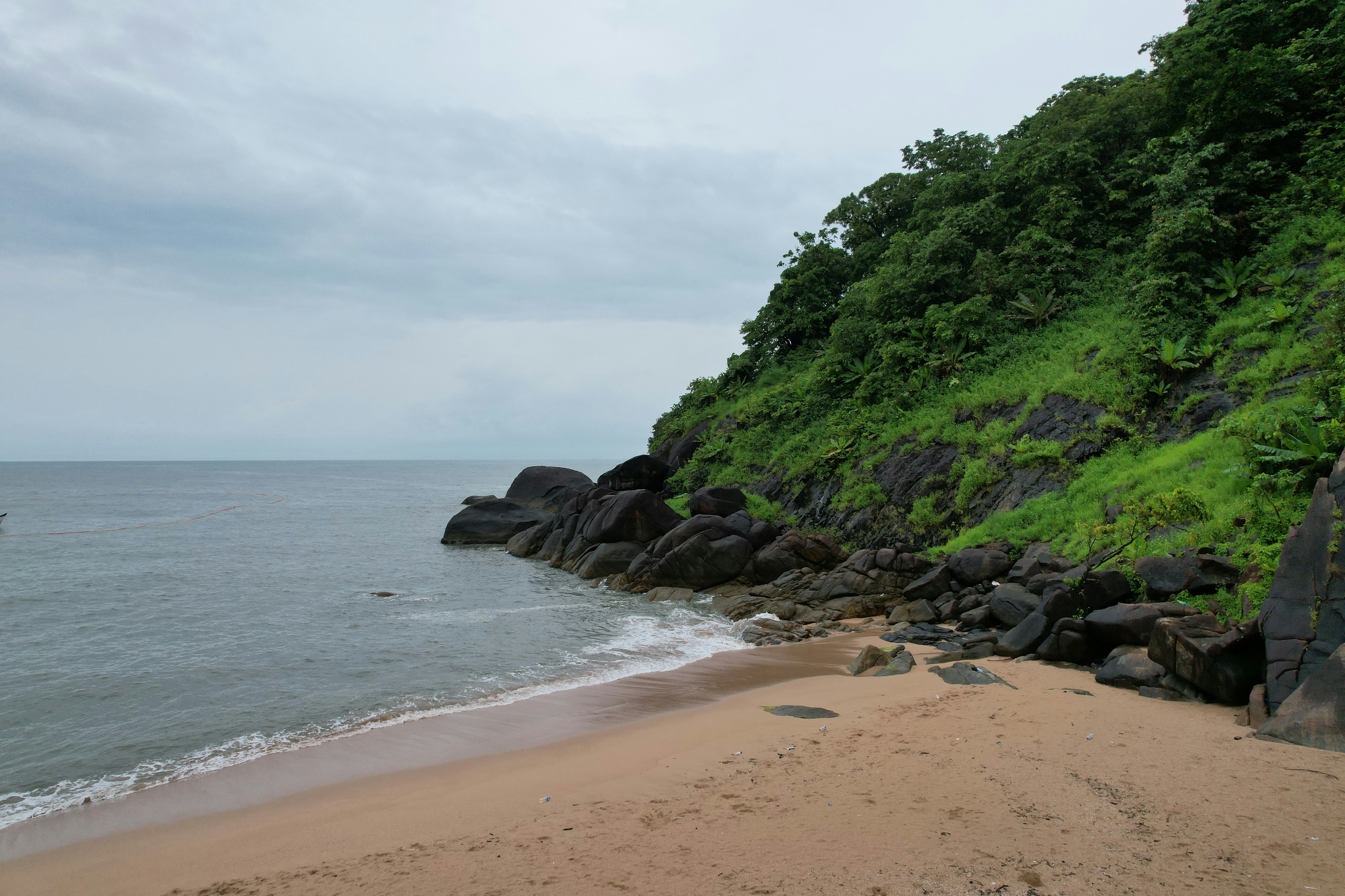 Gentle waves lapping against a sandy beach bordered by lush greenery and rocky cliffs. The tranquil scene captures the essence of a secluded coastal getaway.