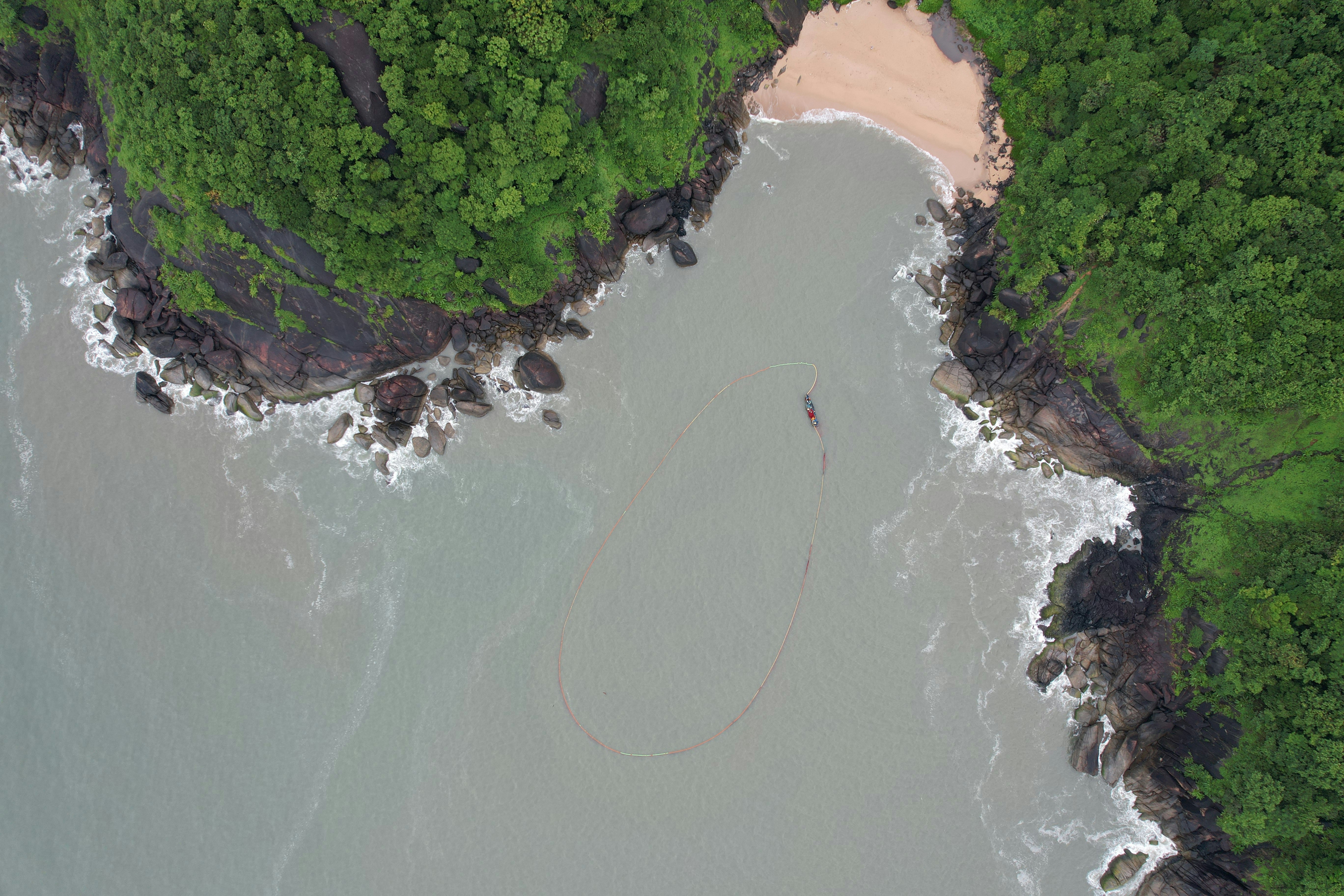 Red Curve over Quiet Coastal Waters: Aerial View of a Cove Between Green Cliffs