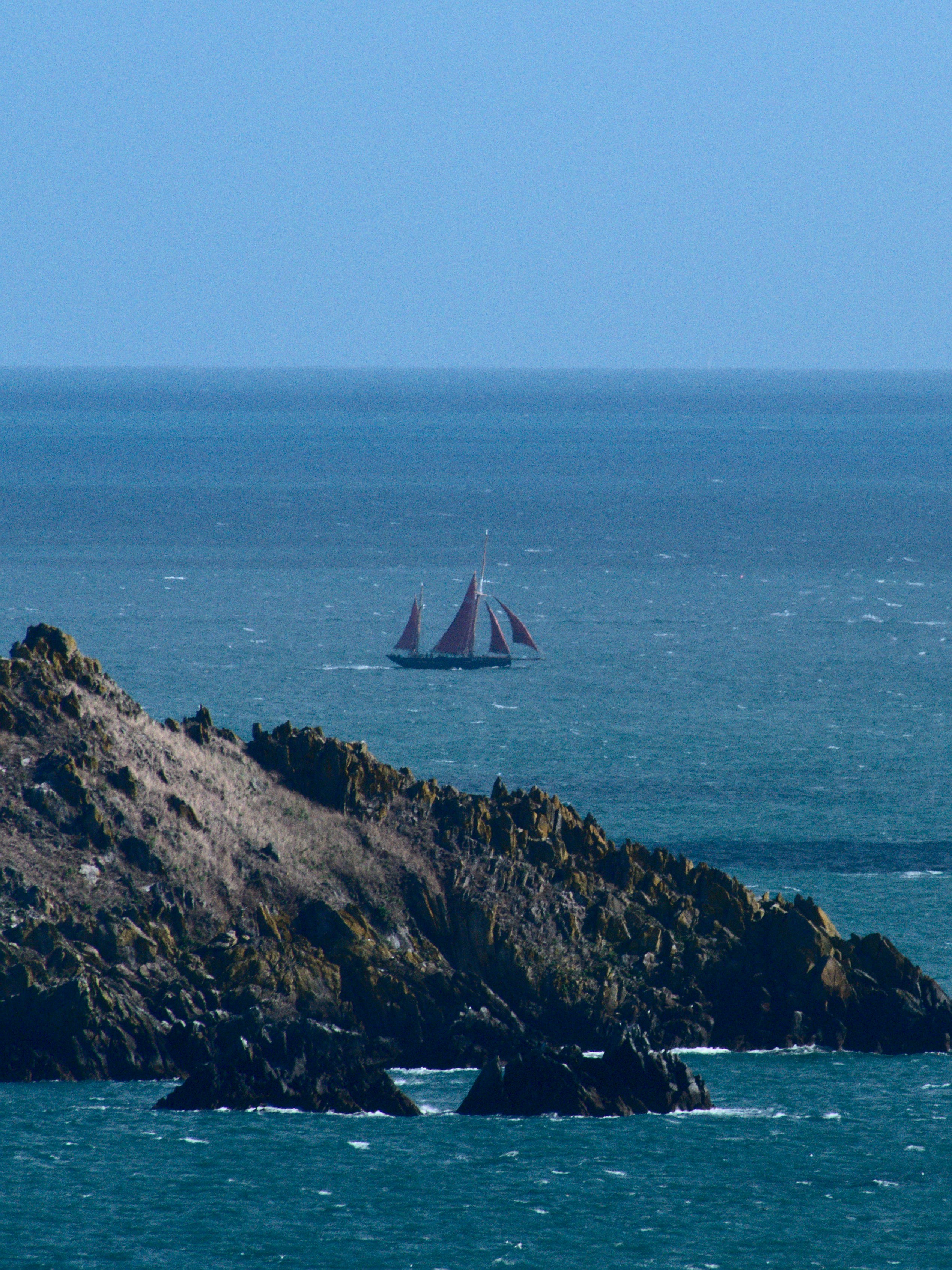 A sailboat sailing in the ocean near a rock outcropping photo – Free ...