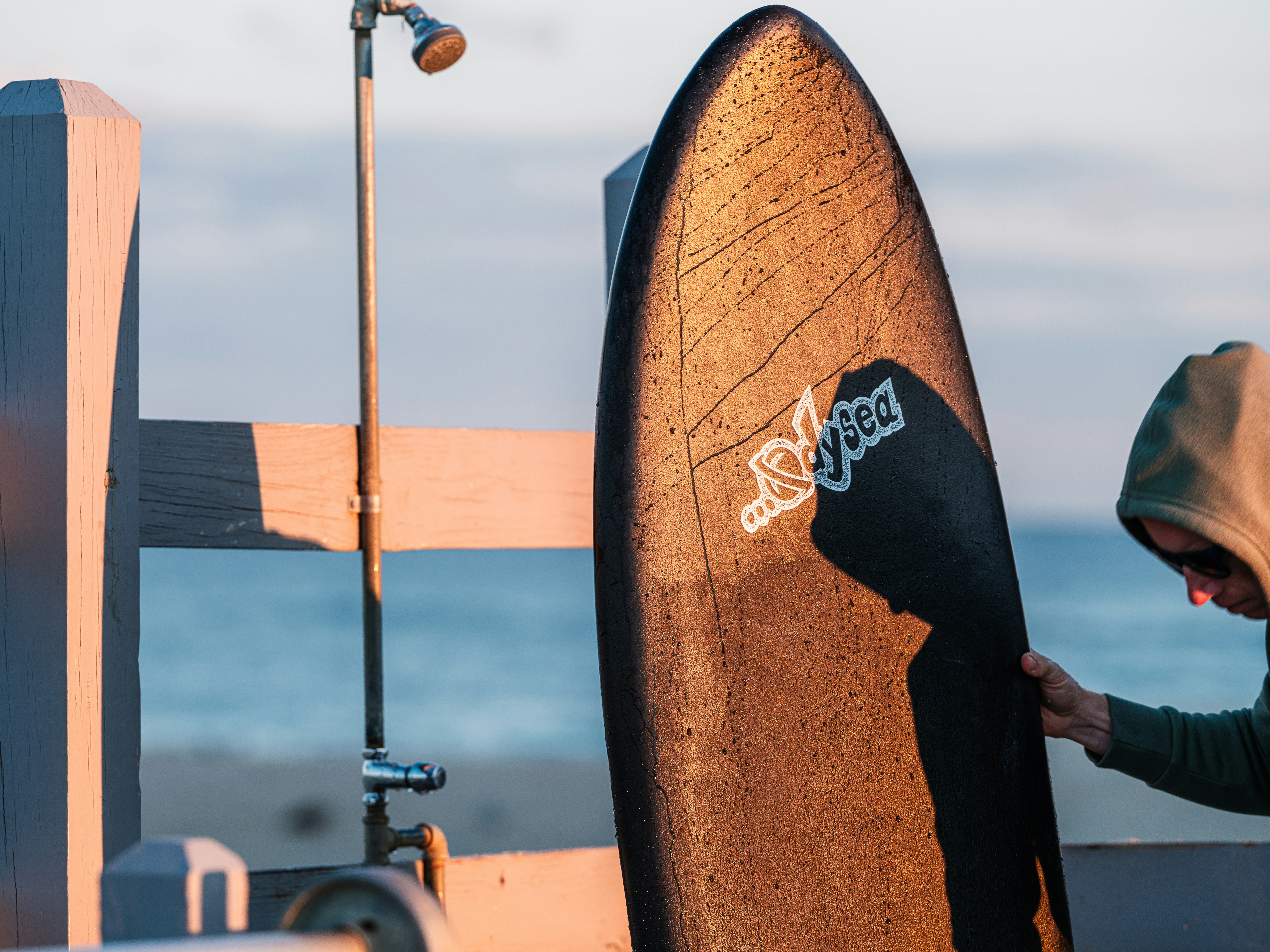 Surfer with Surfboard at Shower Stalls | A man holding a surfboard next to the ocean