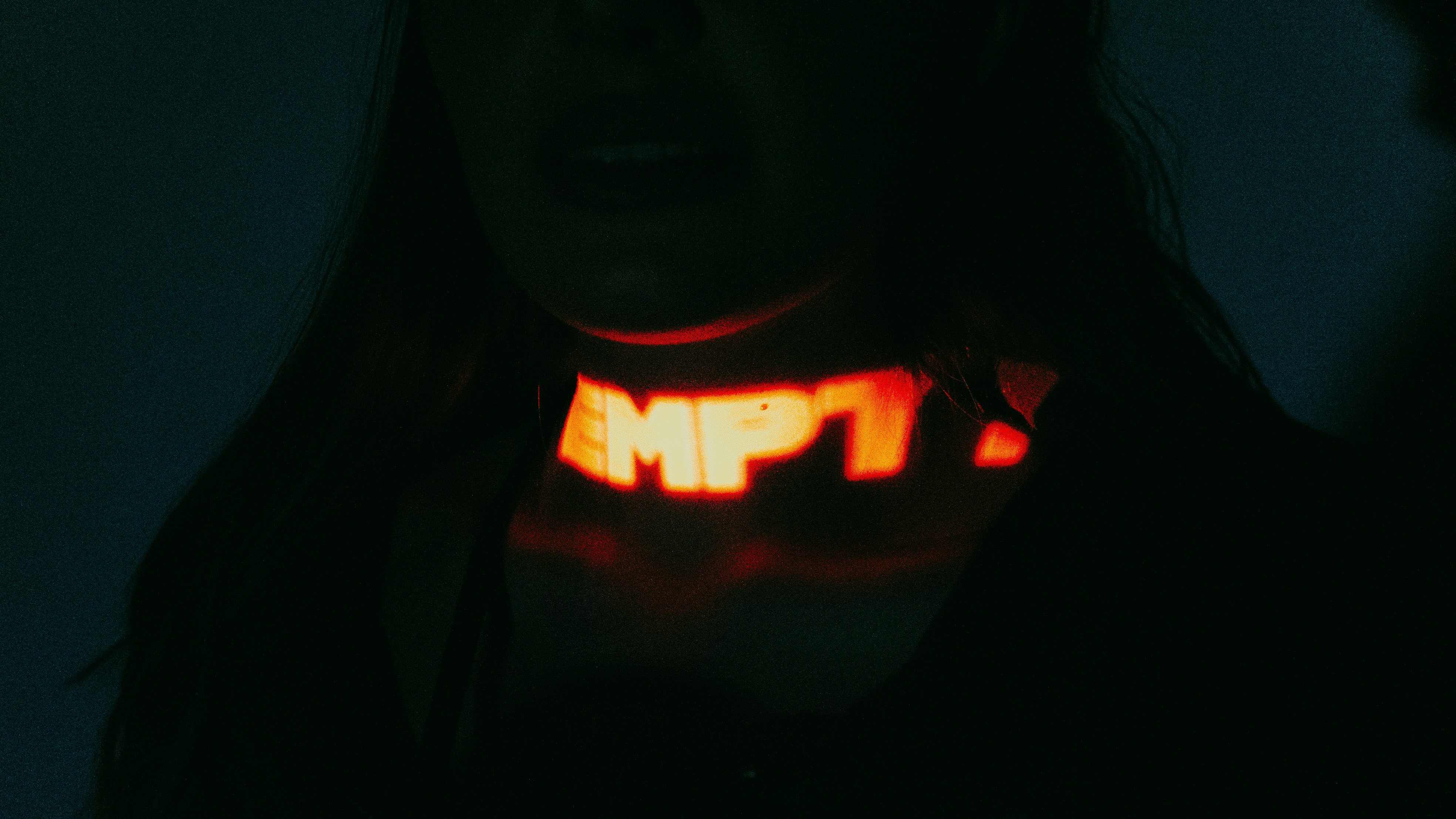 Glowing red text 'EMPTY' projected on a person's neck amidst deep shadows.
