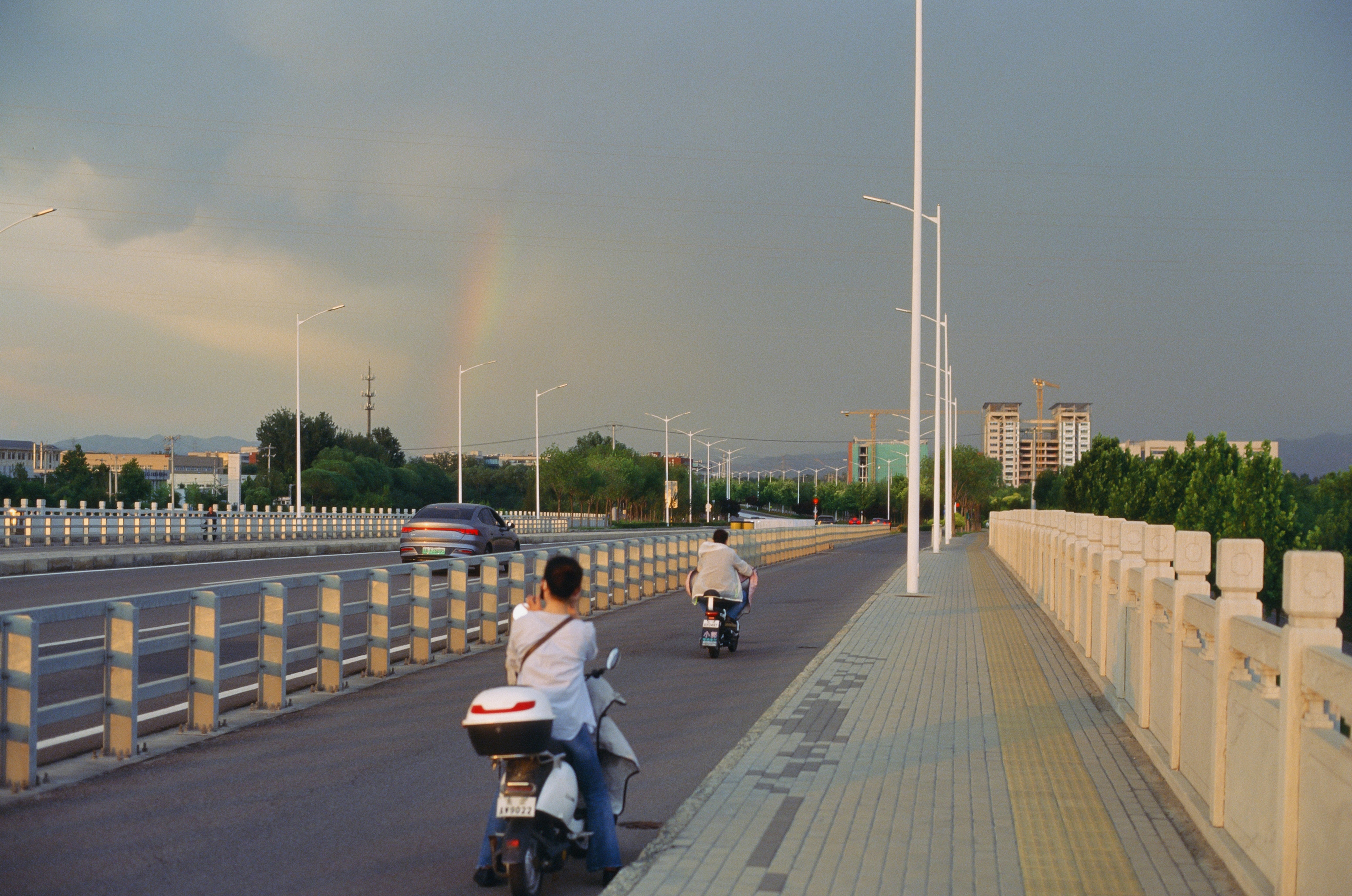 Dusk Commute Under a Faint Rainbow on the Riverside Bridge