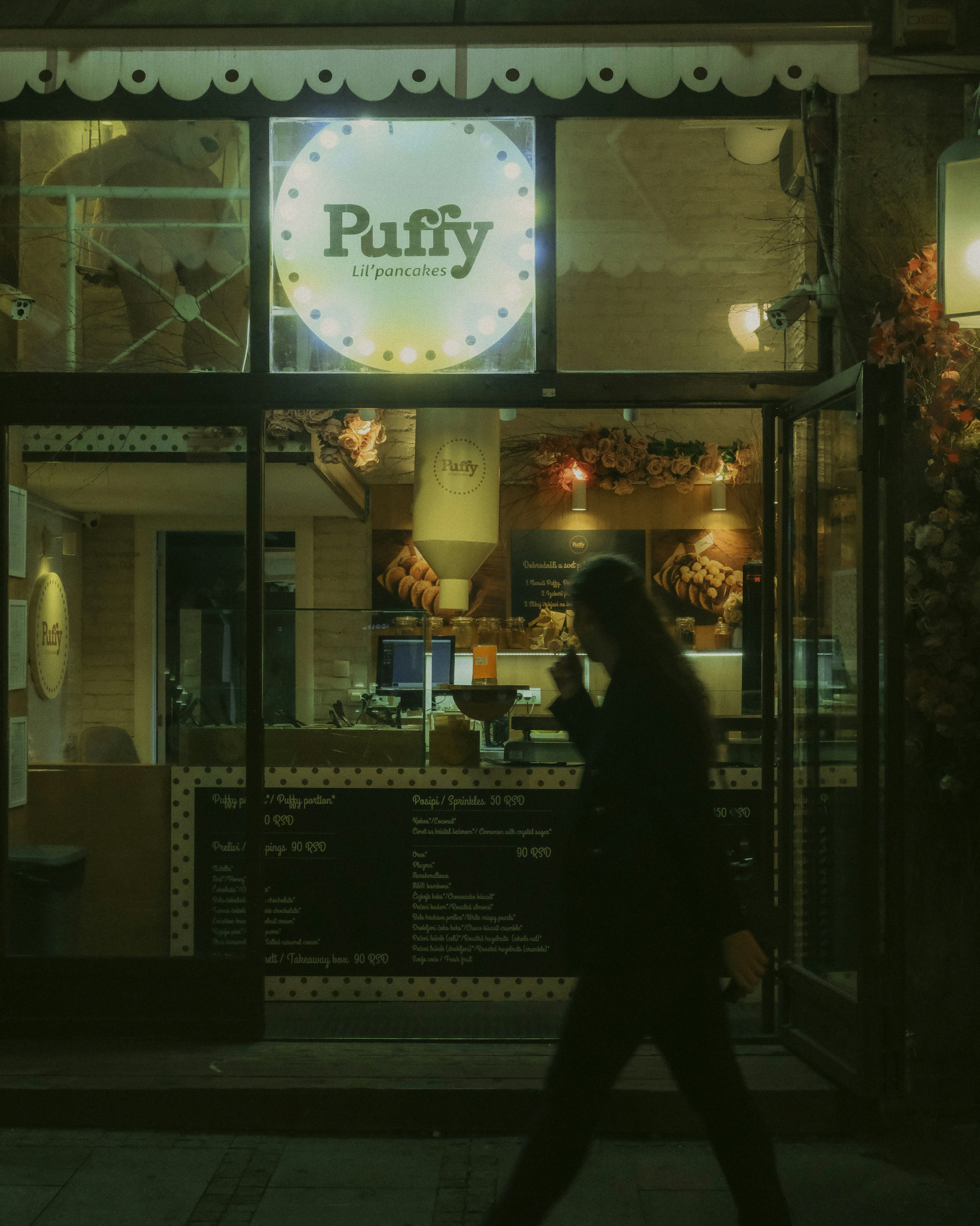Puffy Sign Glow Framed by Storefront Glass as a Pedestrian Passes By