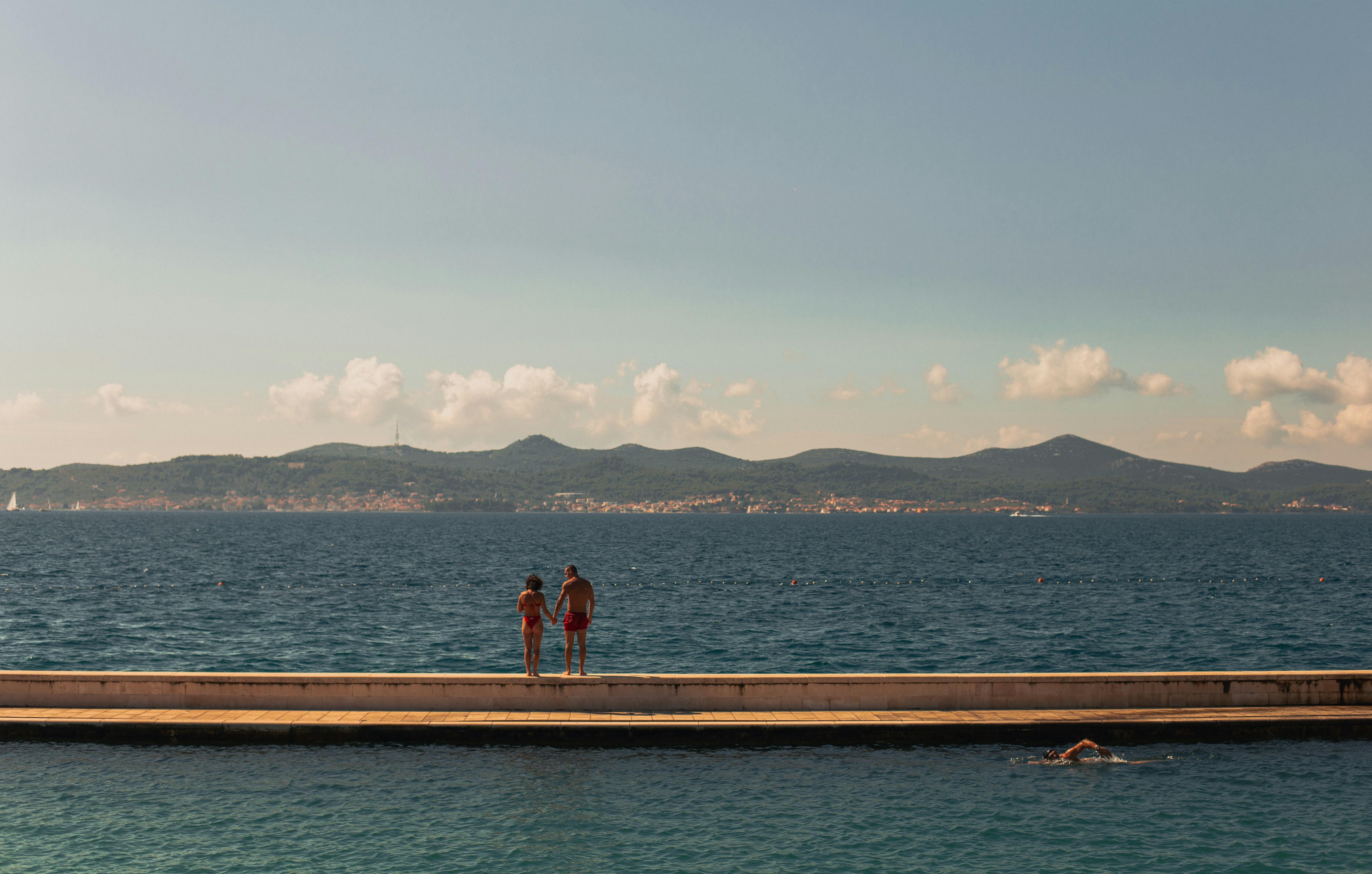 Two silhouetted wanderers at the edge of a seawall under a calm horizon