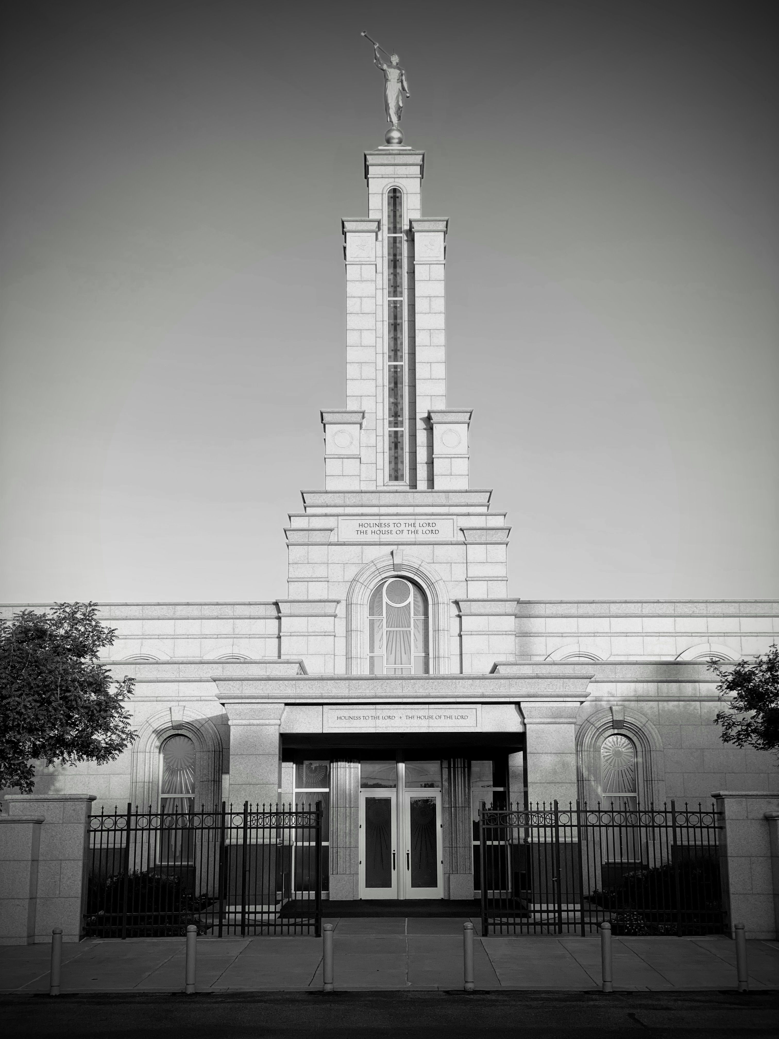 Black and white photograph of a temple with a tall spire and angel statue under a clear sky.