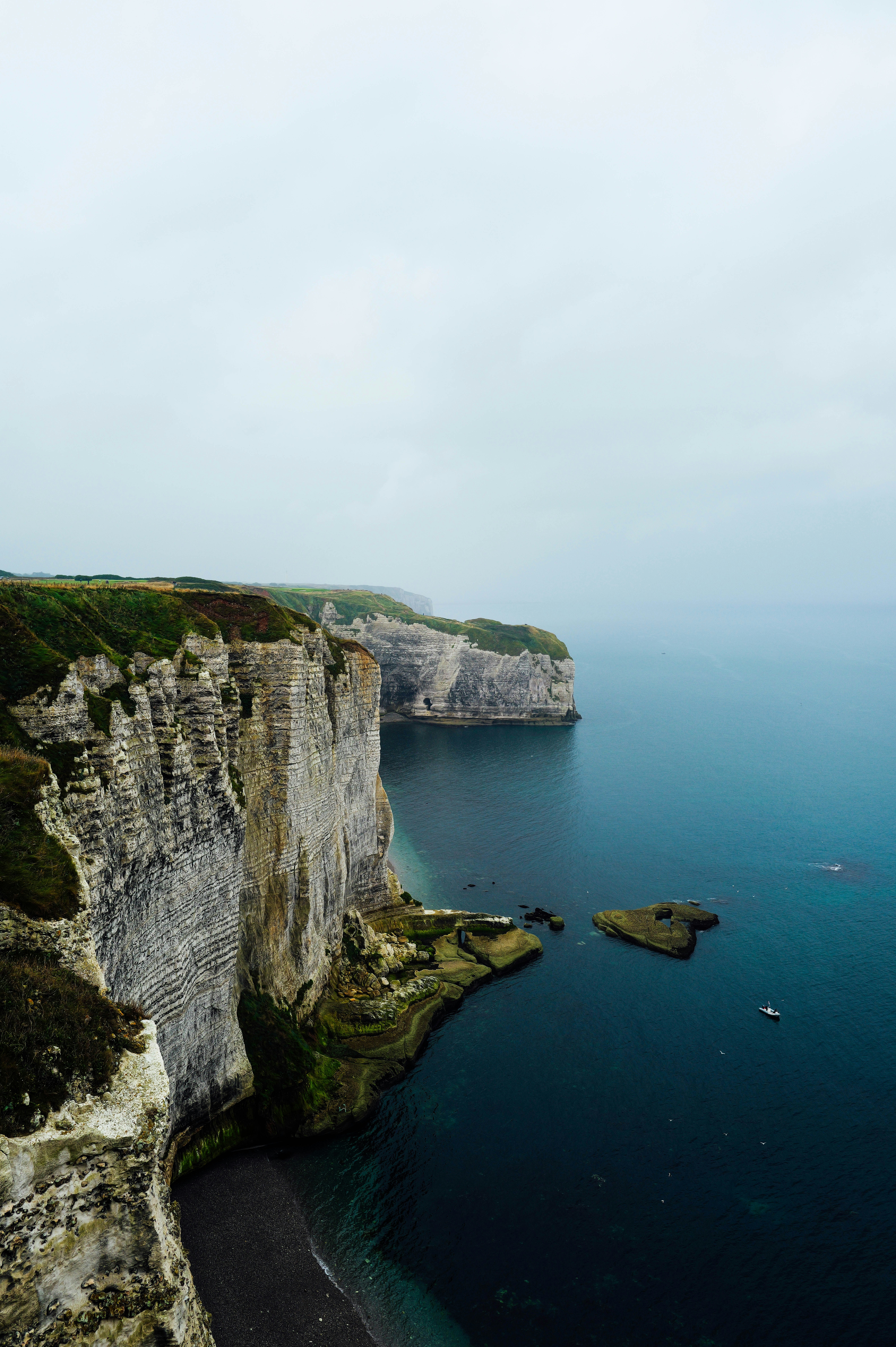 A large body of water next to a rocky cliff photo – Free Cliff Image on ...