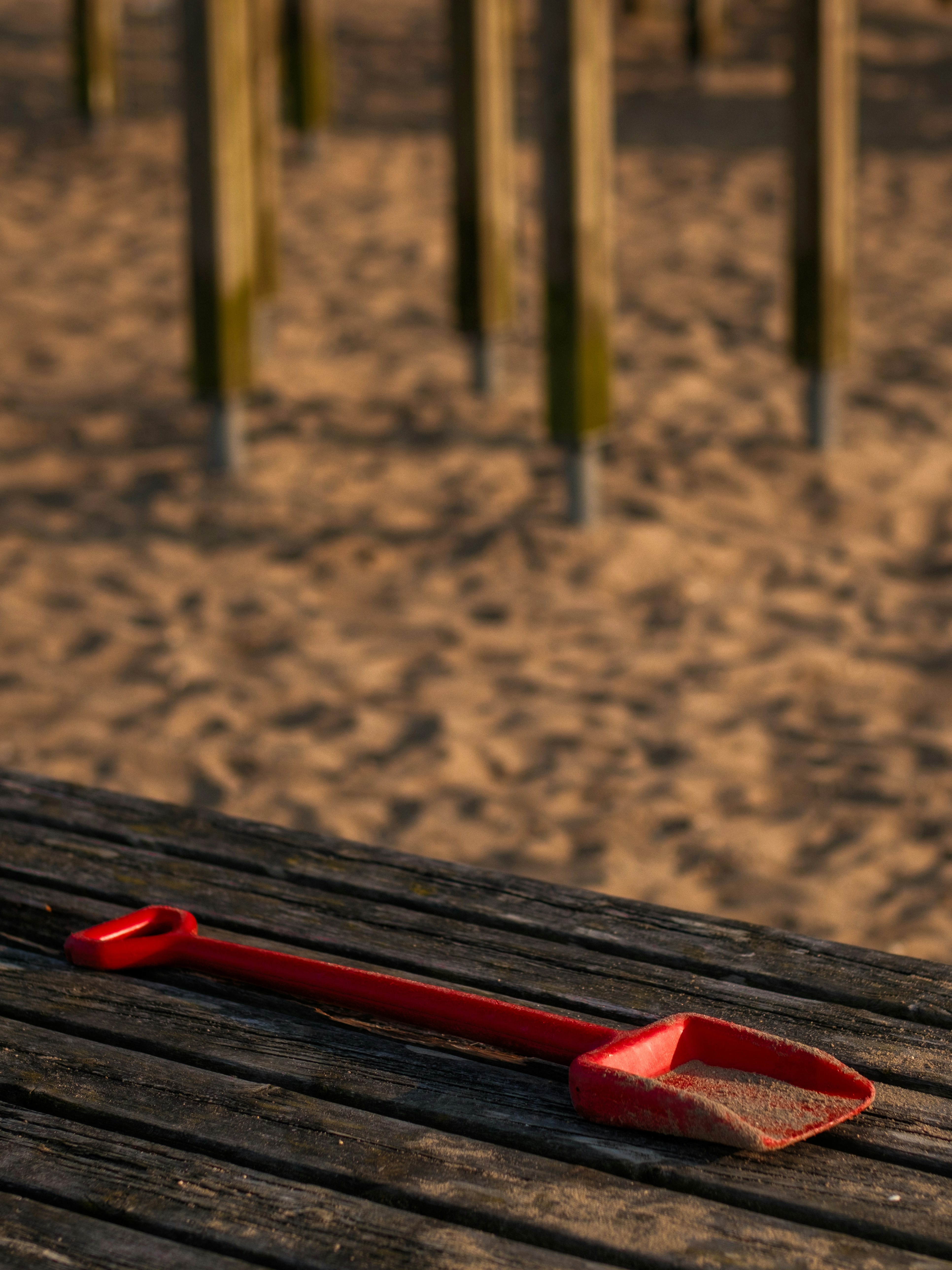 Red Shovel on Weathered Deck as Beach Piers Blur into Sand