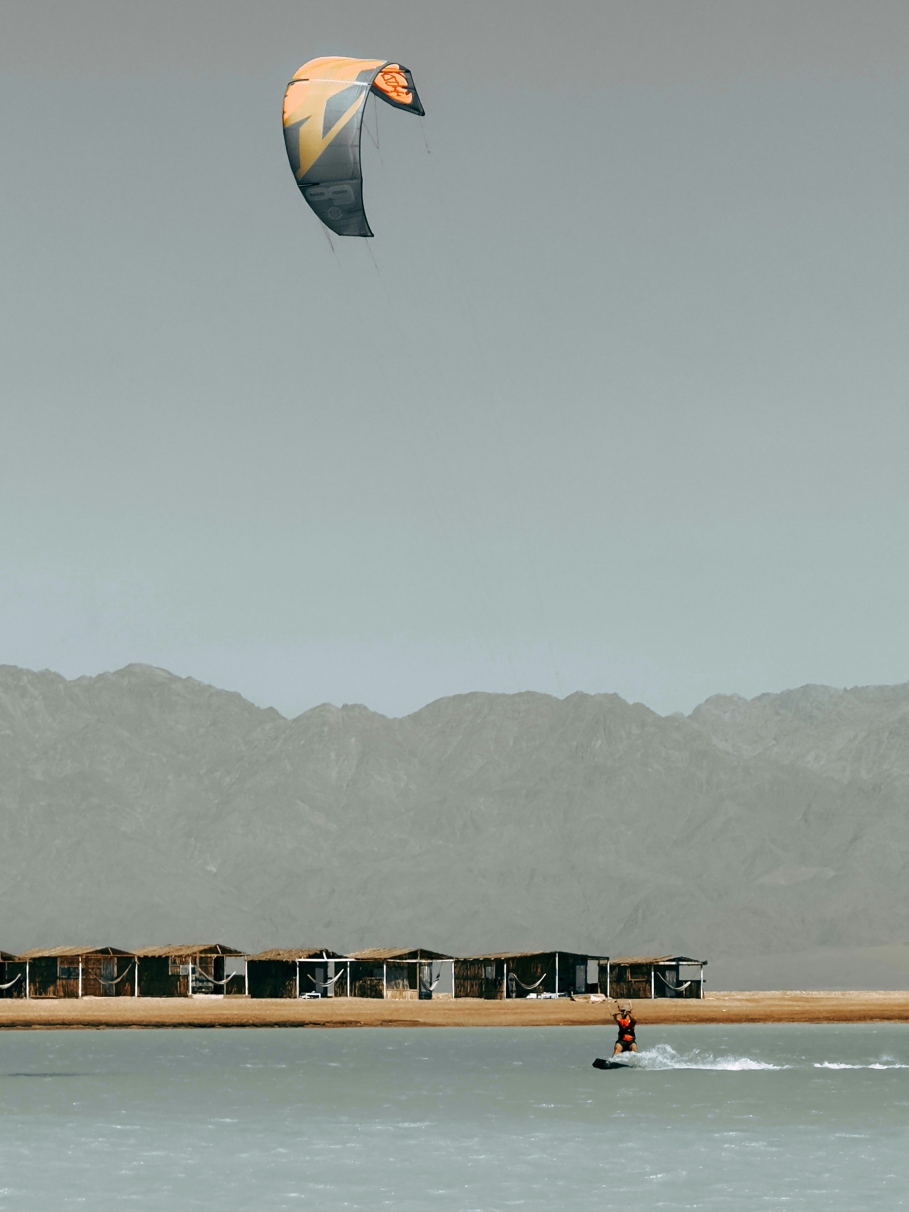 A parasailer glides over the water in front of a mountain range photo ...