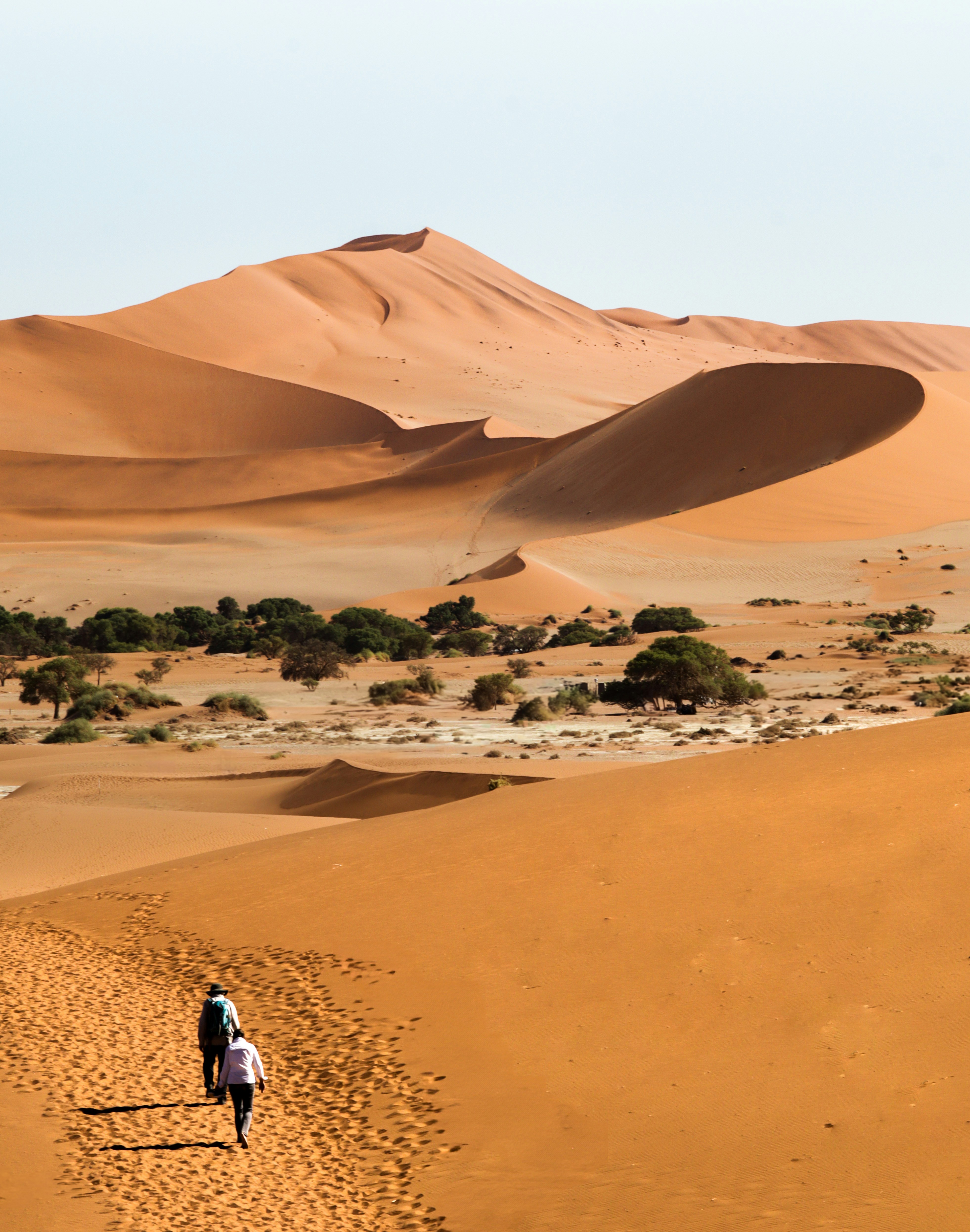 A person walking across a desert with sand dunes in the background