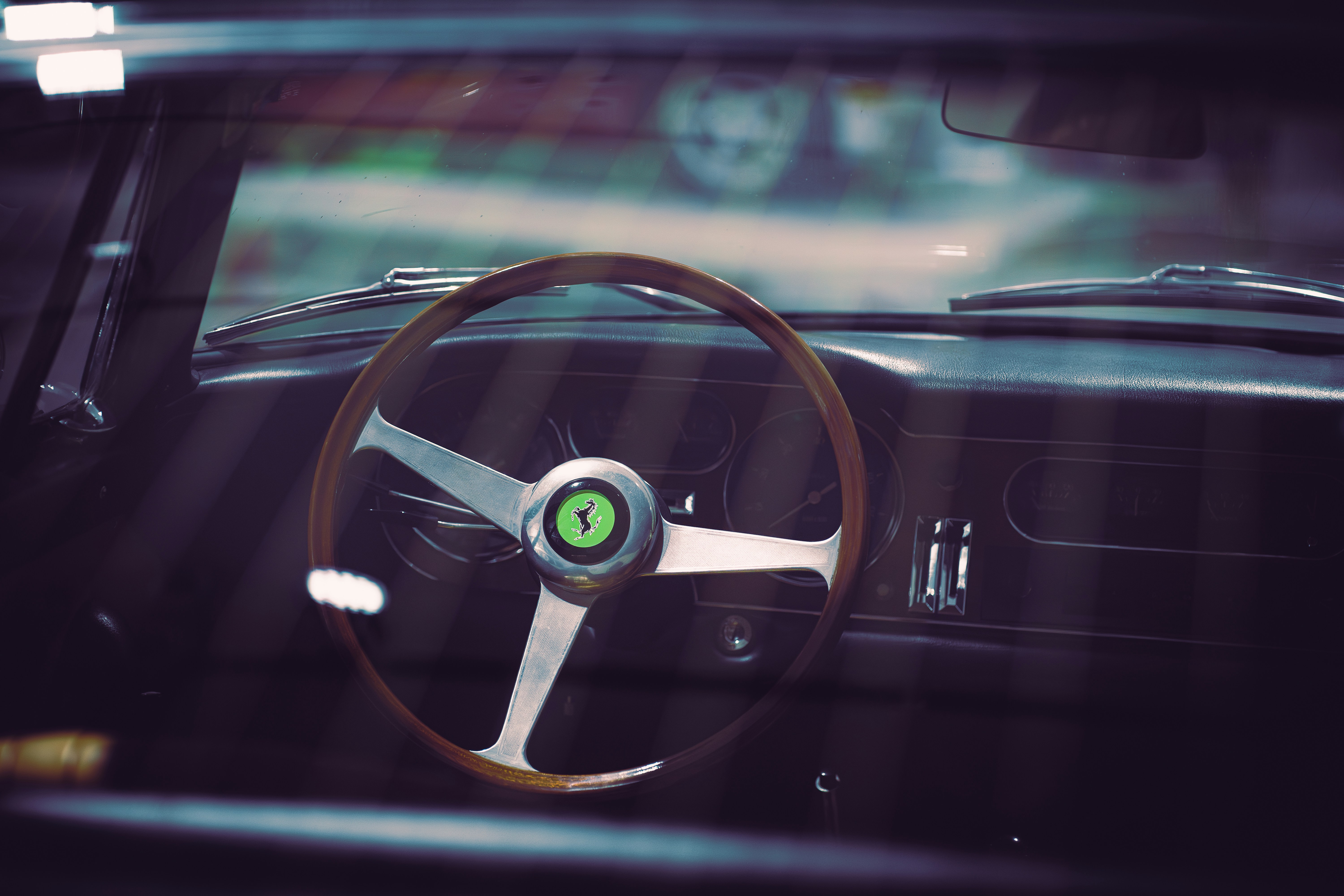 Classic Ferrari steering wheel with a polished wooden rim and iconic emblem, set against a sleek dashboard.