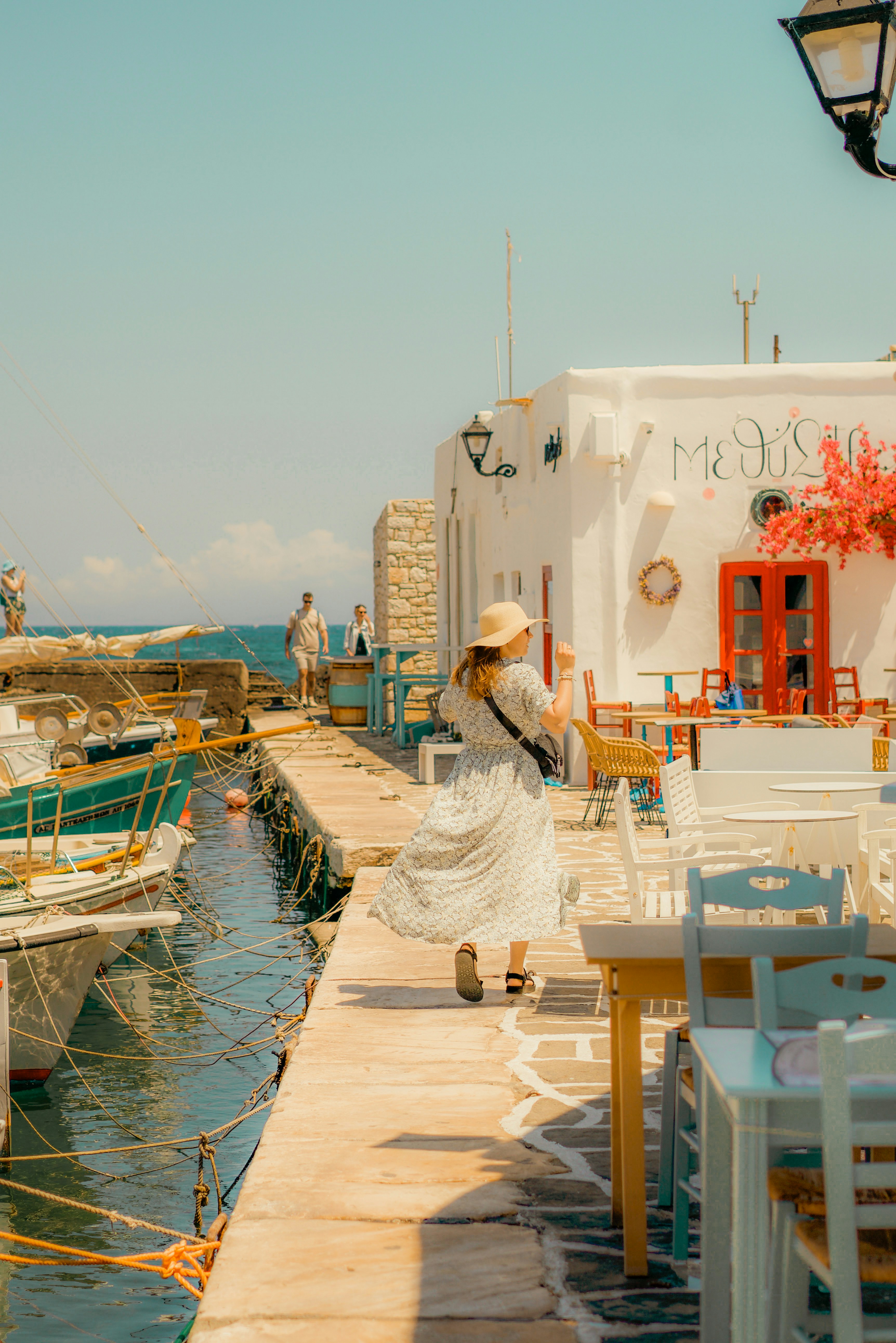 Sunlit Harborside Stroll: A Woman in Straw Hat by the White Café