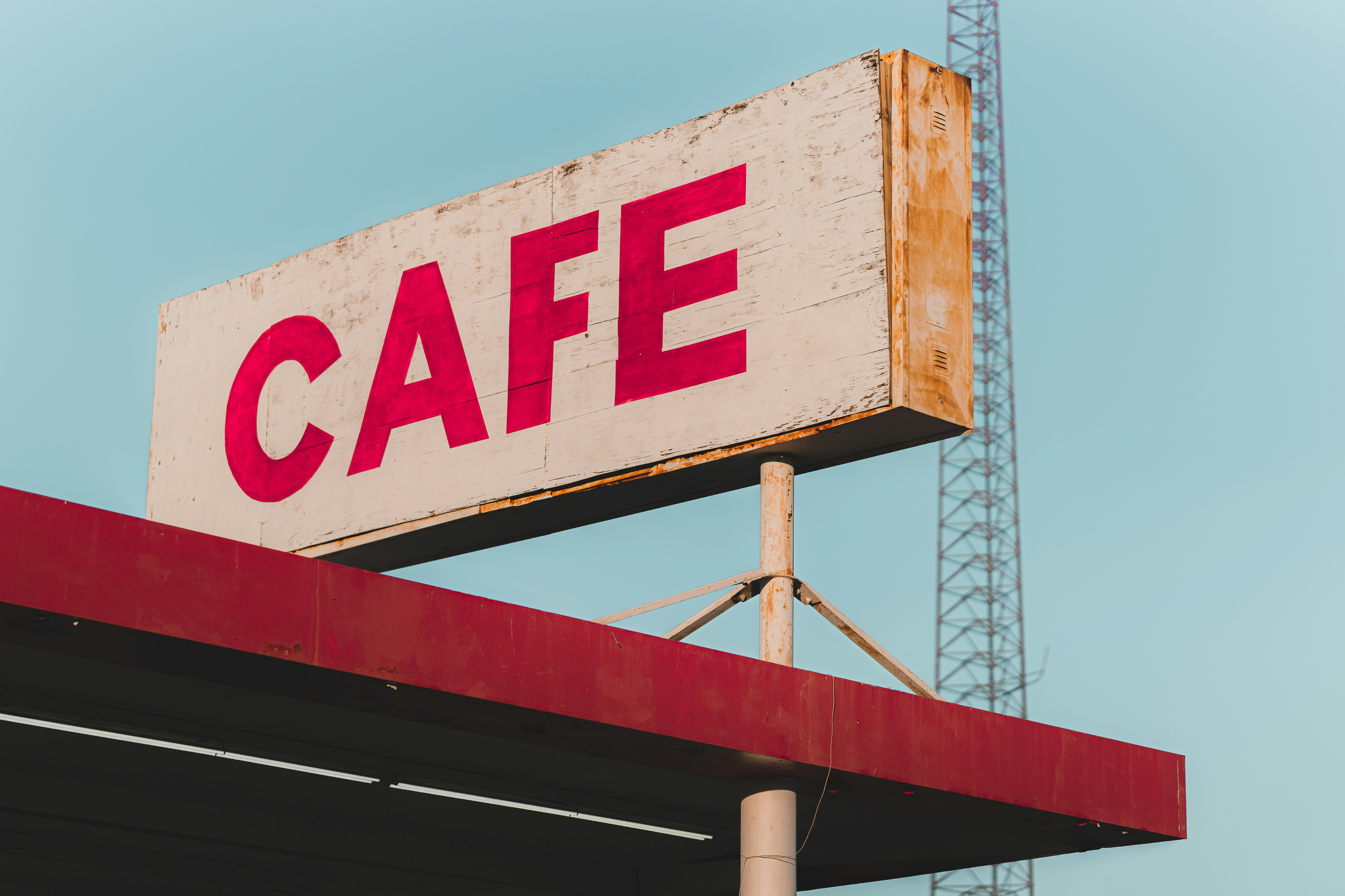 Rustic cafe sign perched on a building rooftop under a pale blue sky.