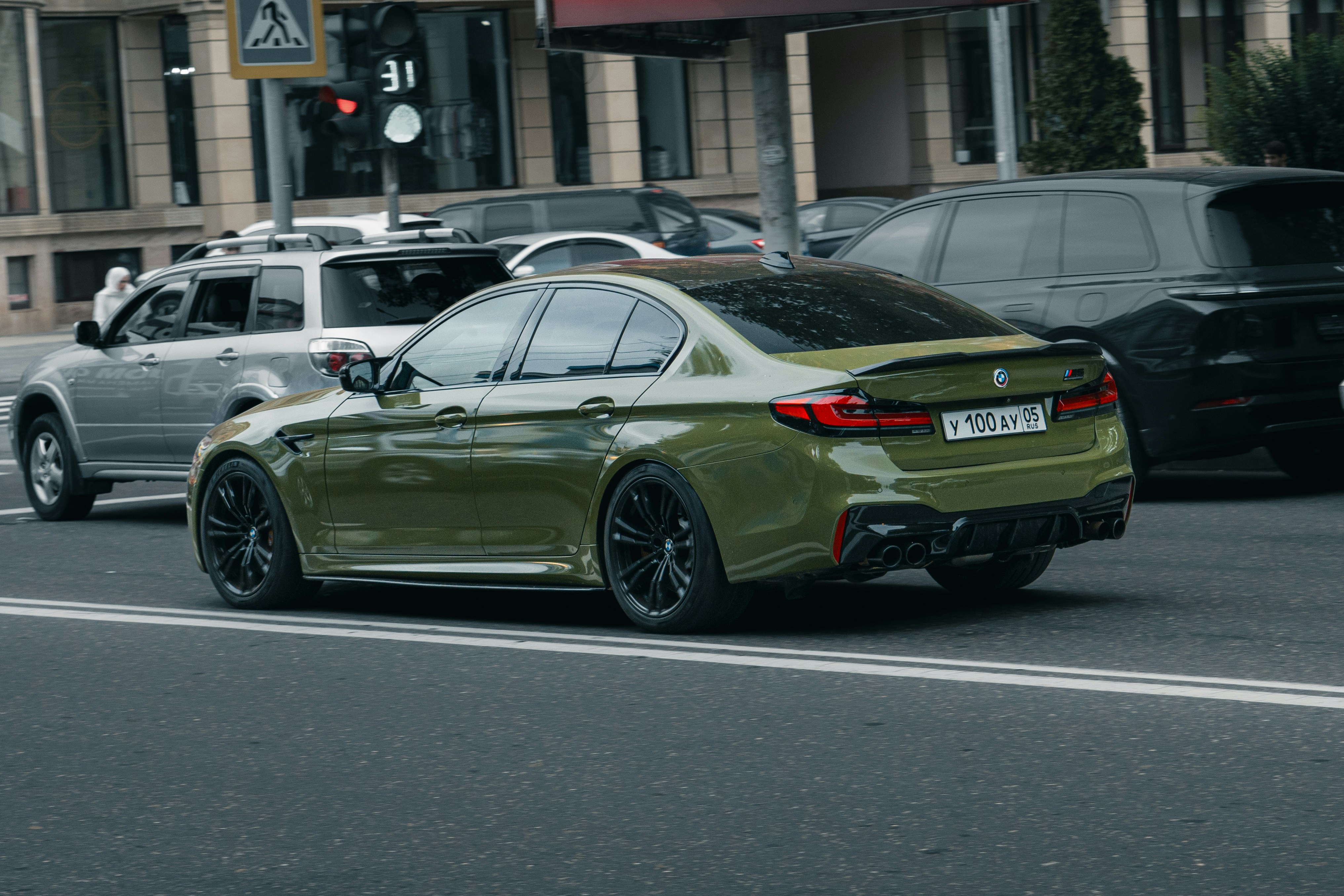 A green car driving down a street next to a traffic light photo – Free ...