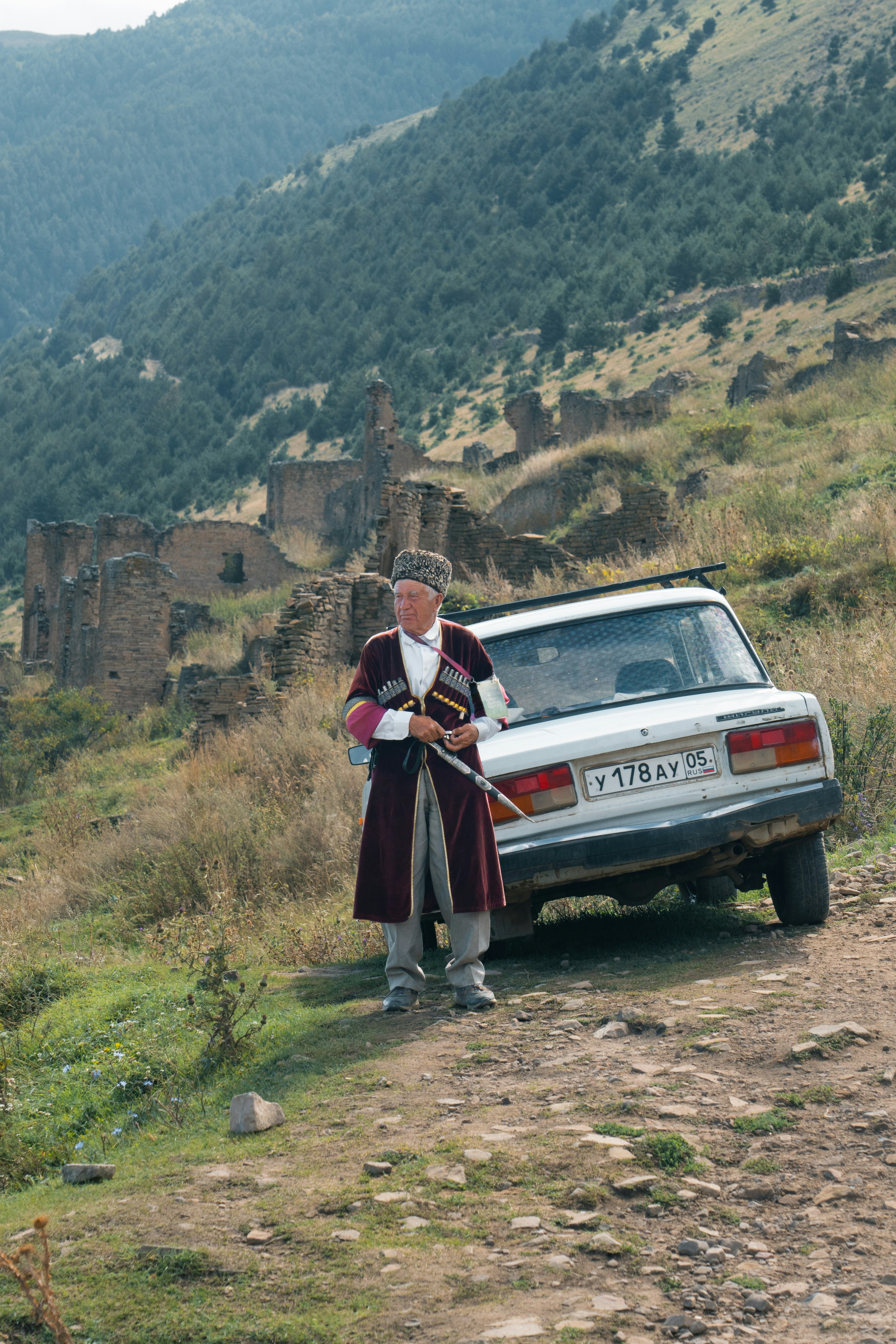 A man standing next to a car on a dirt road