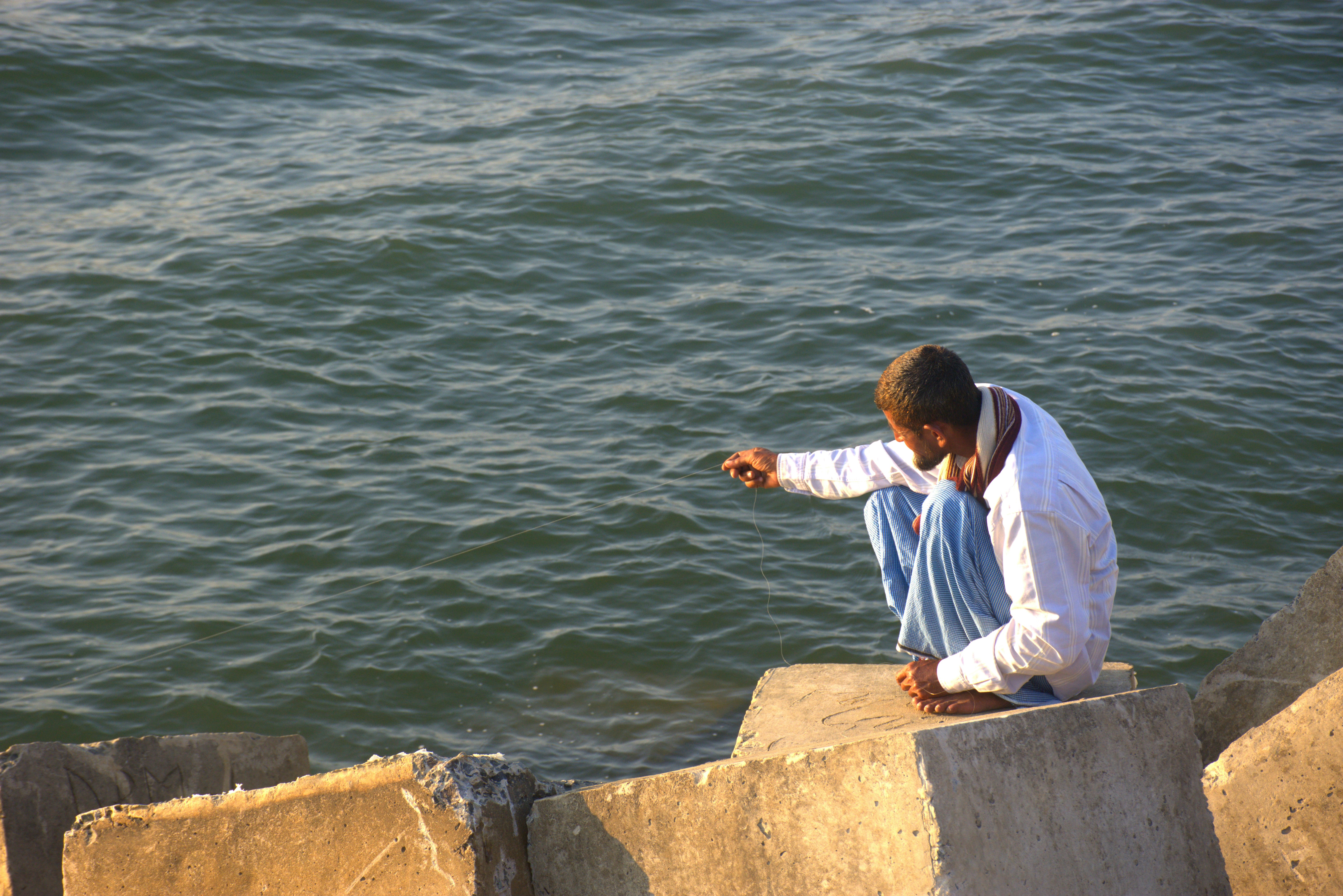 Edge-of-Water Gaze: A lone figure on a sunlit breakwater