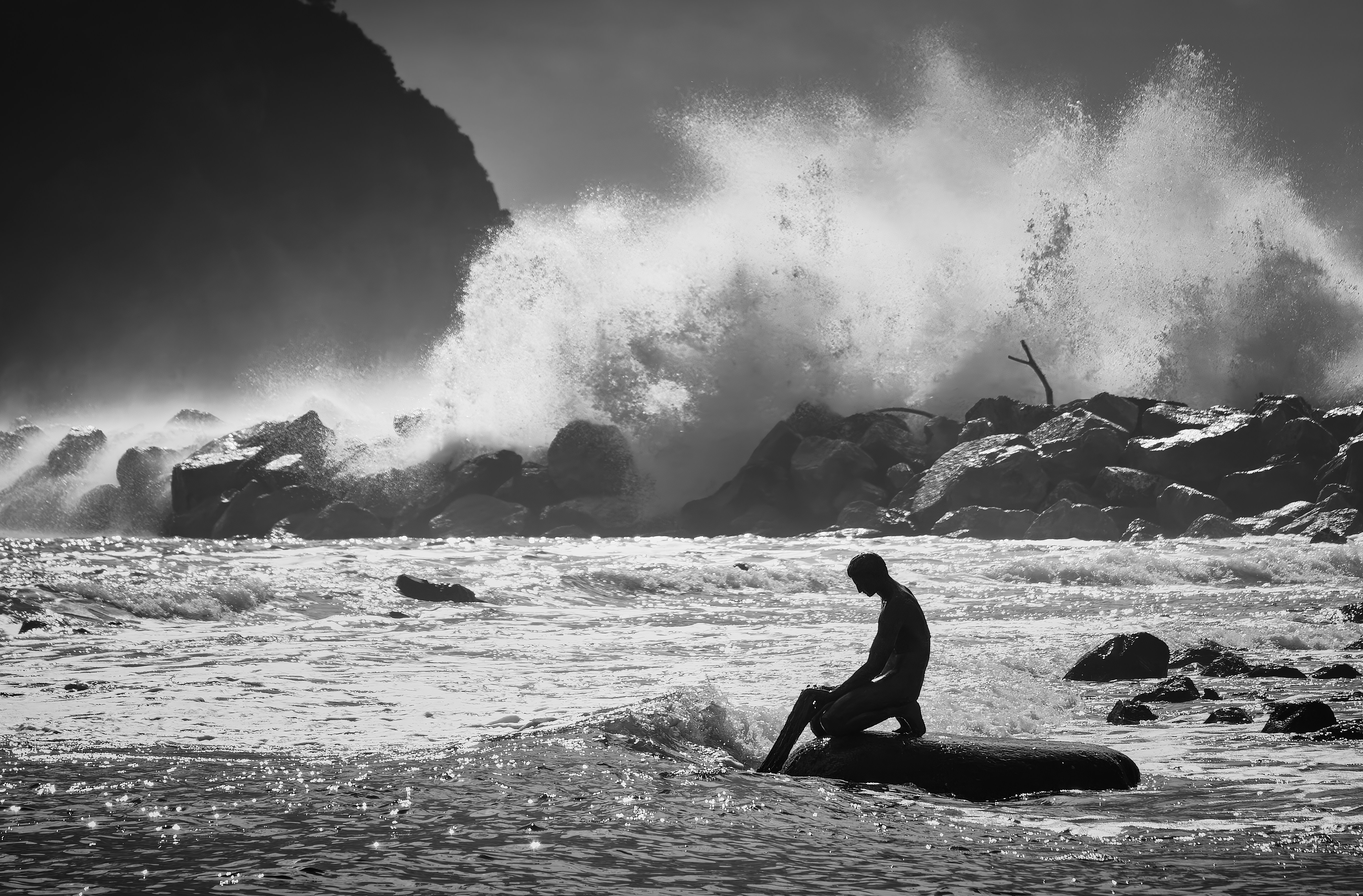 Silhouette of a person sitting on a rock with crashing waves in the background.