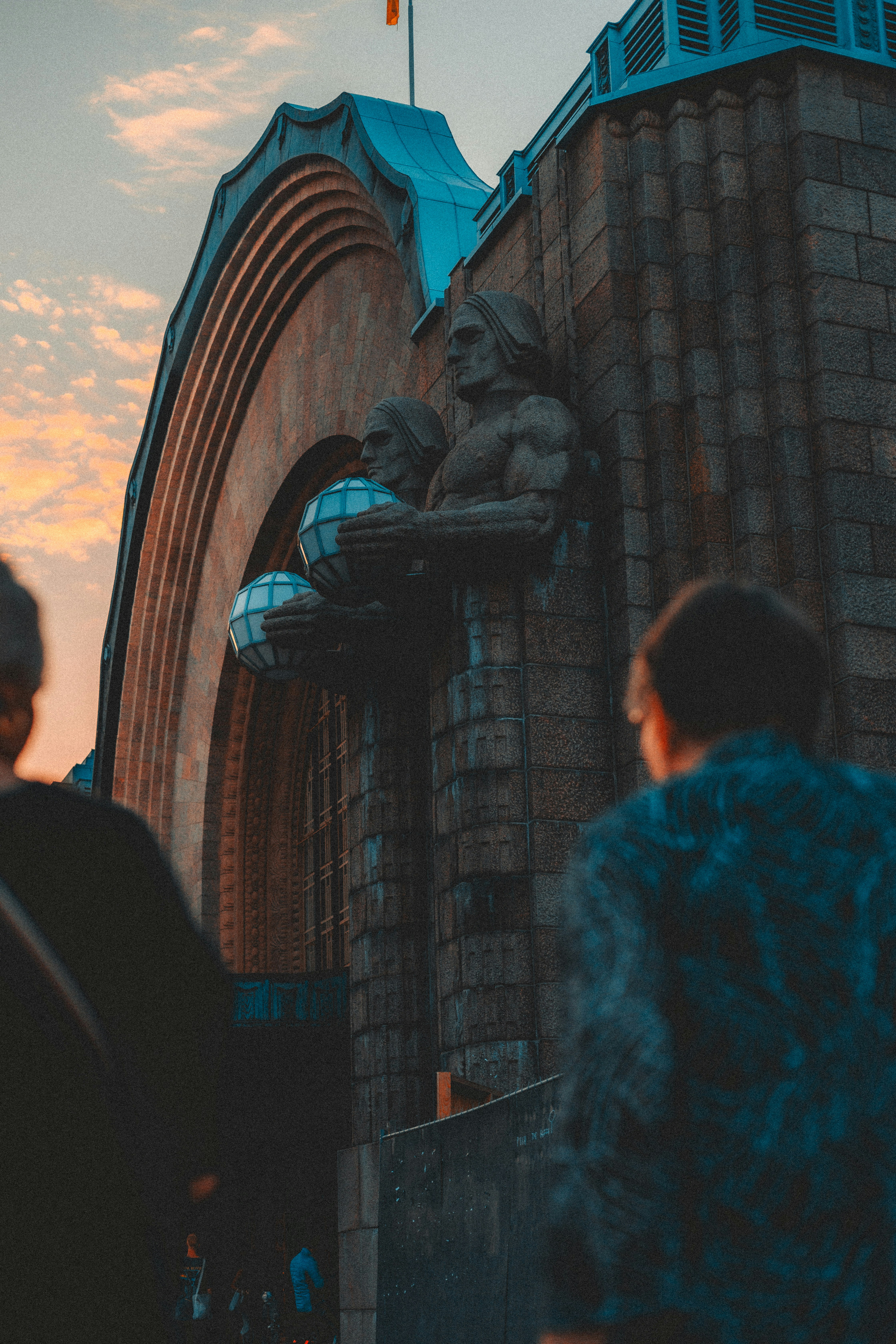 Statues and silhouettes at sunset: lanterns and arches framing a civic entrance