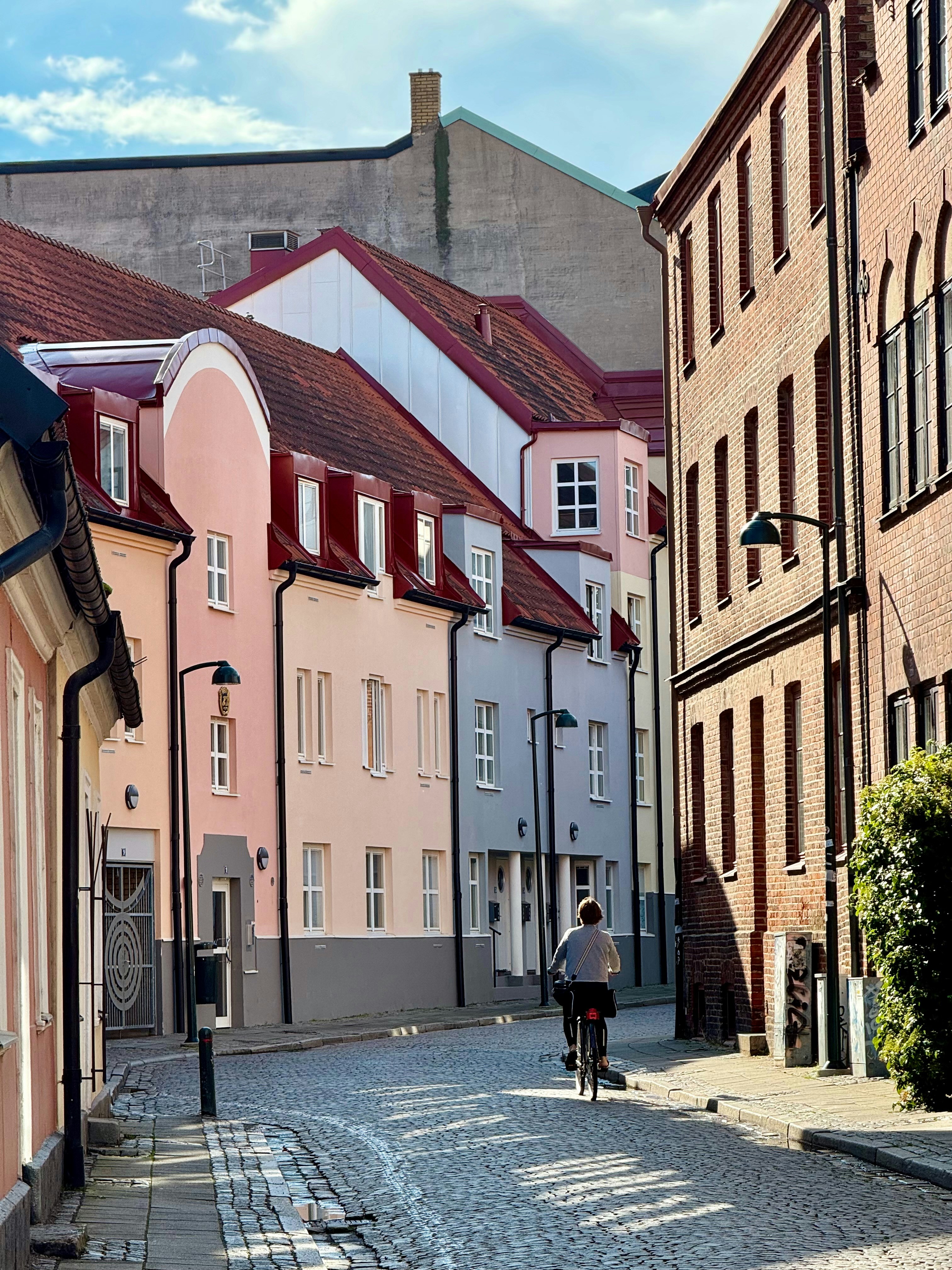 Cyclist on a cobblestone street lined with pastel-colored buildings in Lund, Sweden.