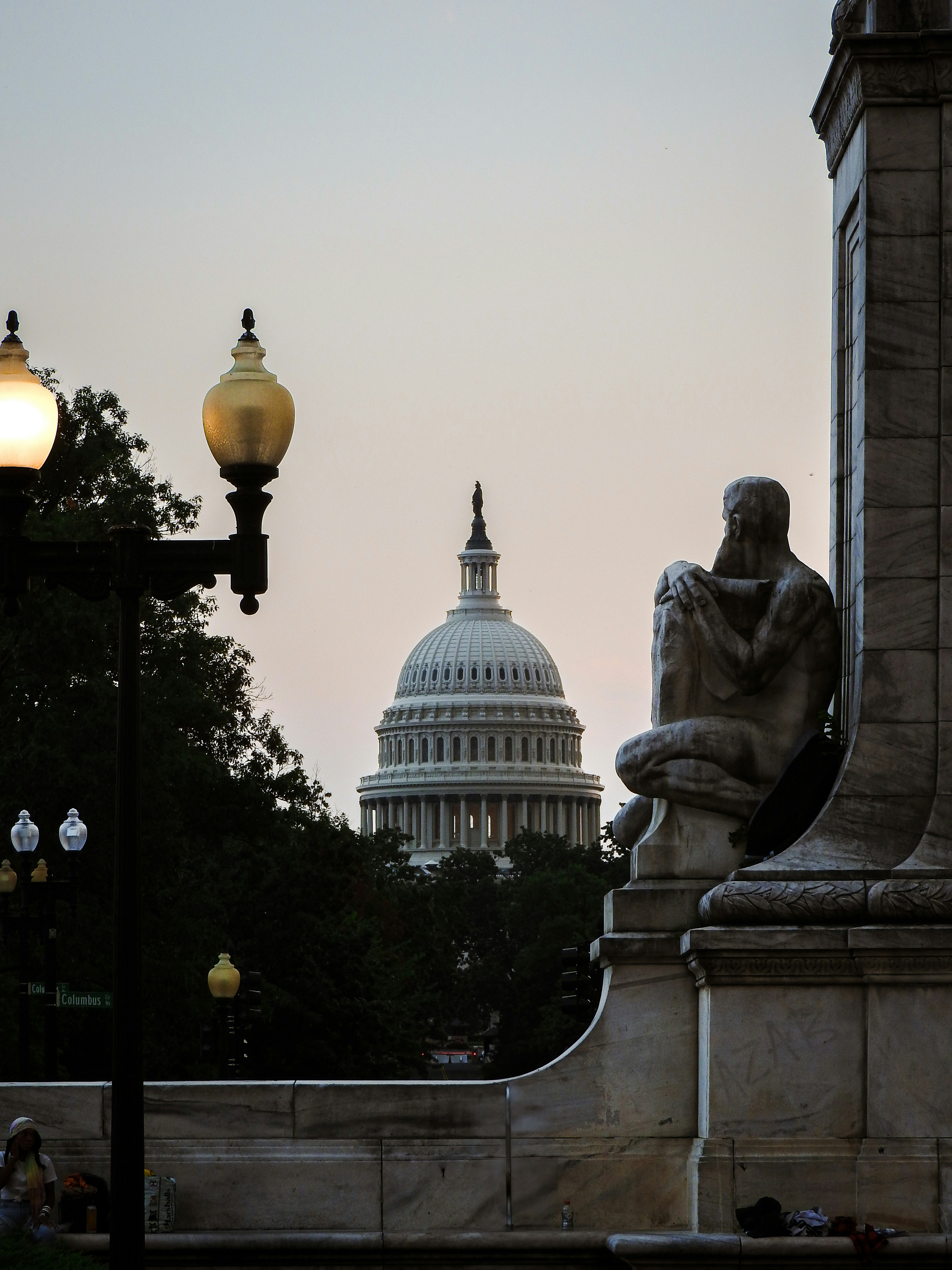 A statue in the foreground frames the U.S. Capitol dome, highlighting the contrast between art and architecture in a tranquil evening setting.